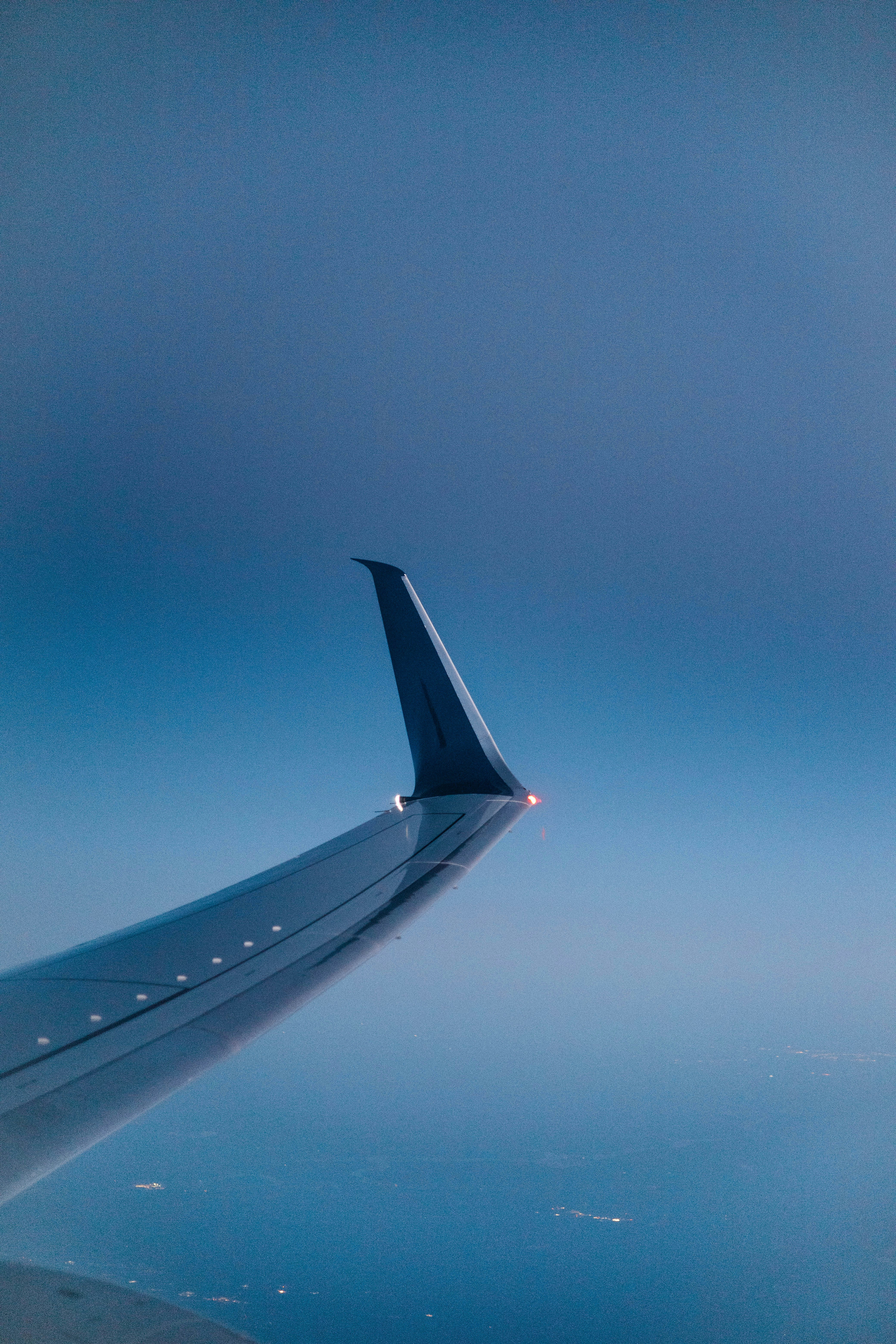 Airplane wing gliding through a serene twilight sky, with distant lights twinkling below. The horizon blends seamlessly into the fading light.