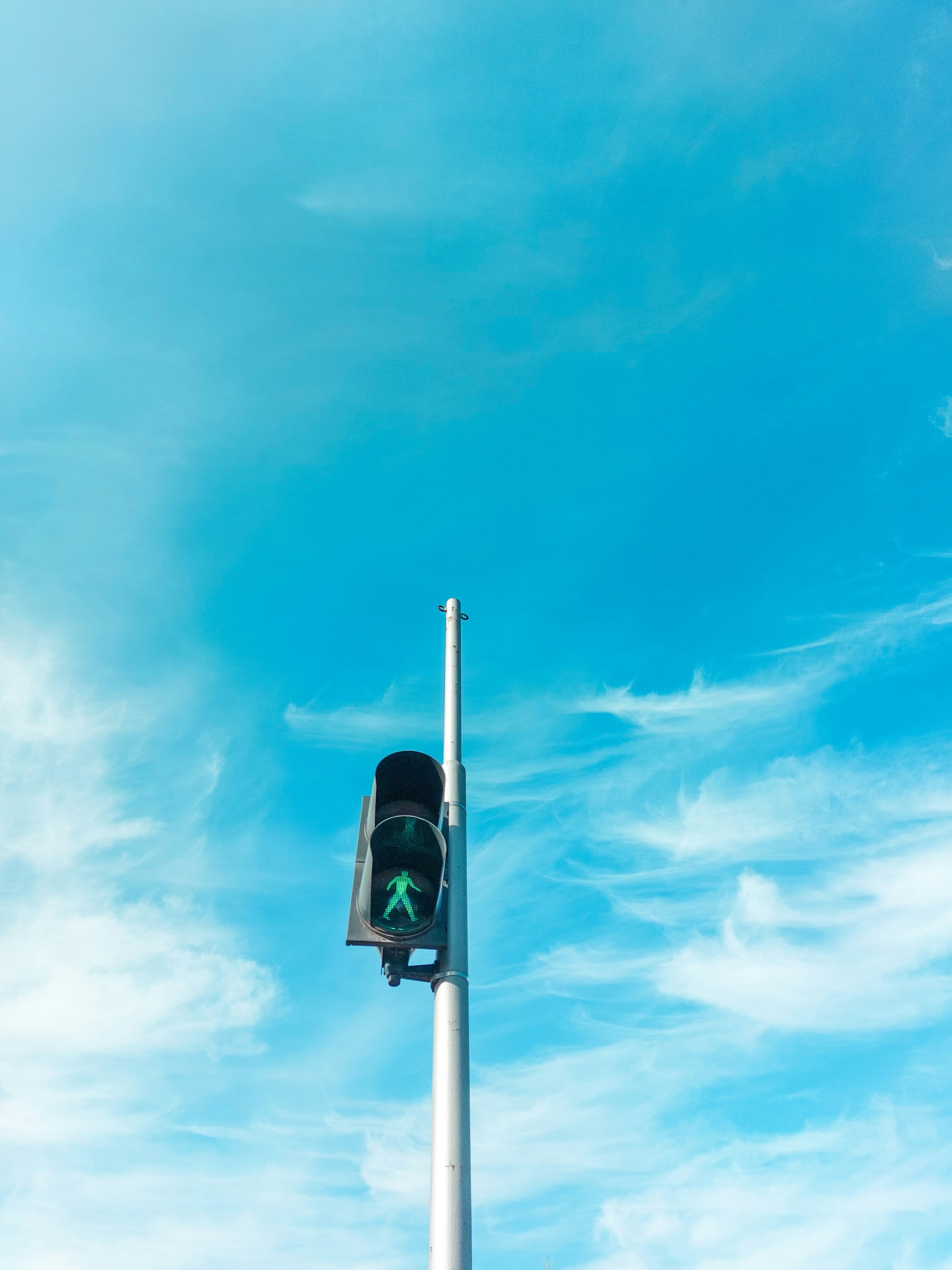 Green pedestrian traffic light against a bright blue sky with wispy clouds.
