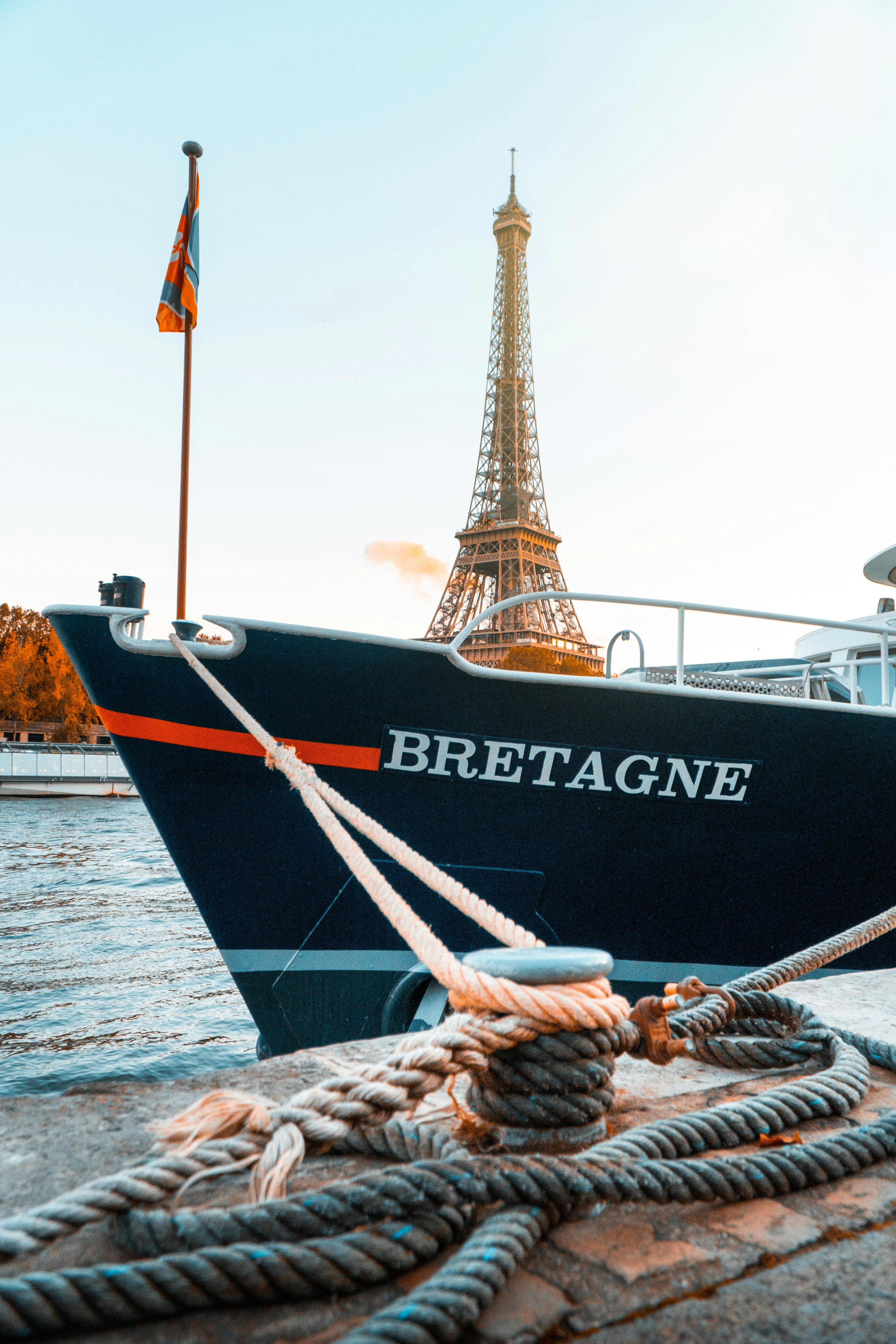 A boat named 'BRETAGNE' moored by the Seine, with the Eiffel Tower rising majestically in the background. The scene captures the essence of Parisian waterways.