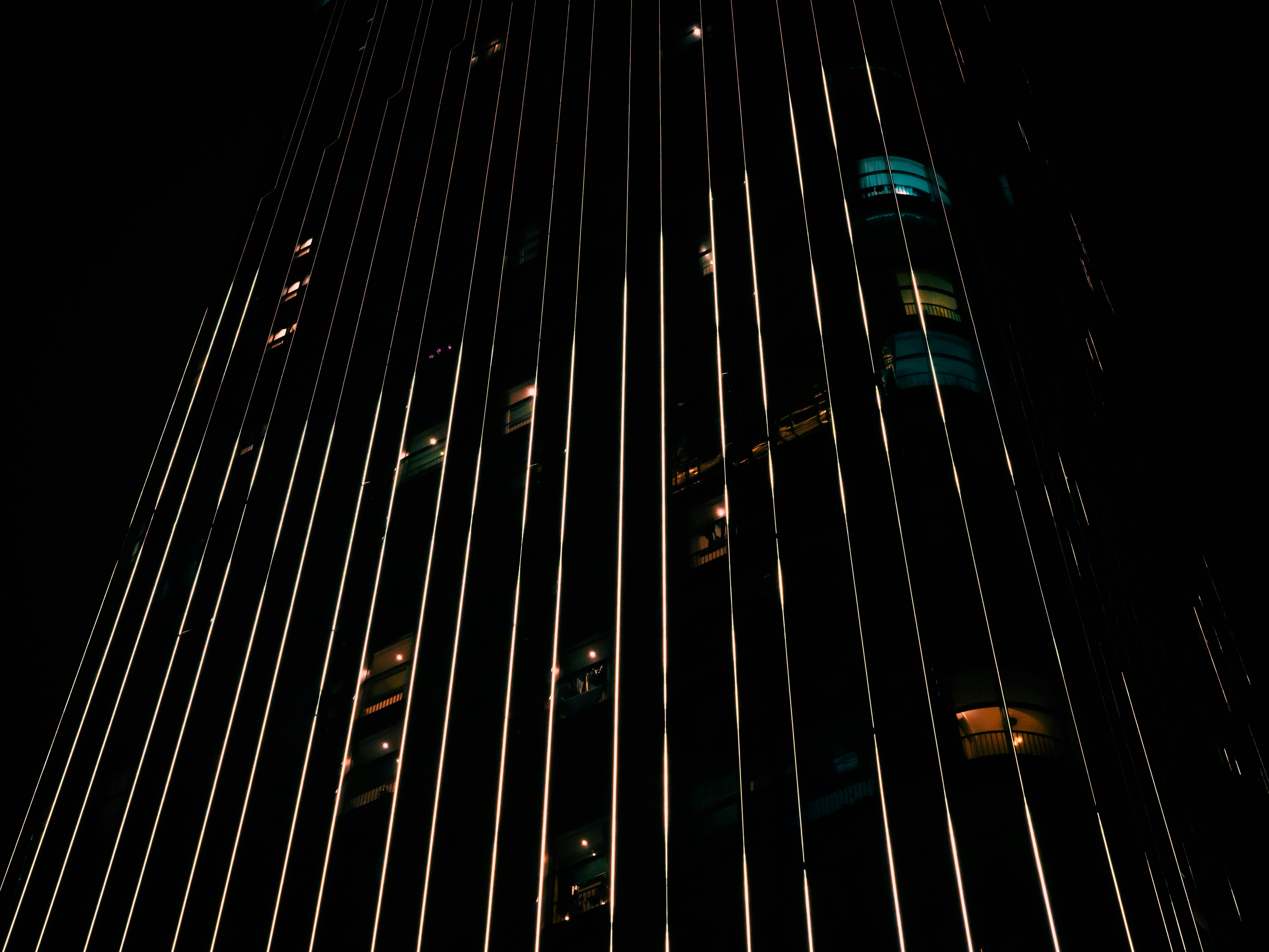 Vertical lines of light accentuate the modern architecture of a high-rise building at night, revealing glimpses of illuminated windows.