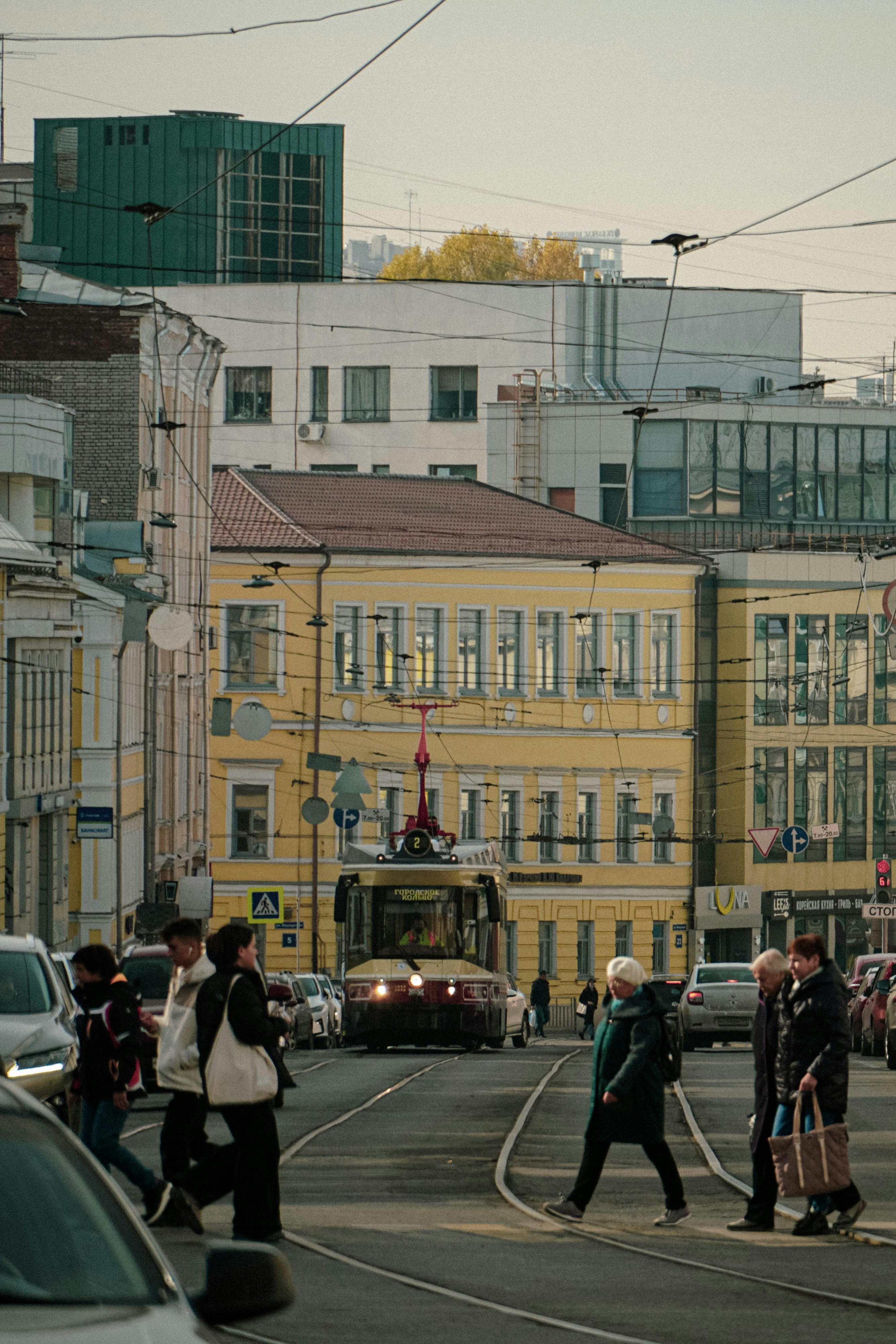 Tram navigating through a bustling city street as pedestrians cross the tracks, framed by modern and historic architecture.