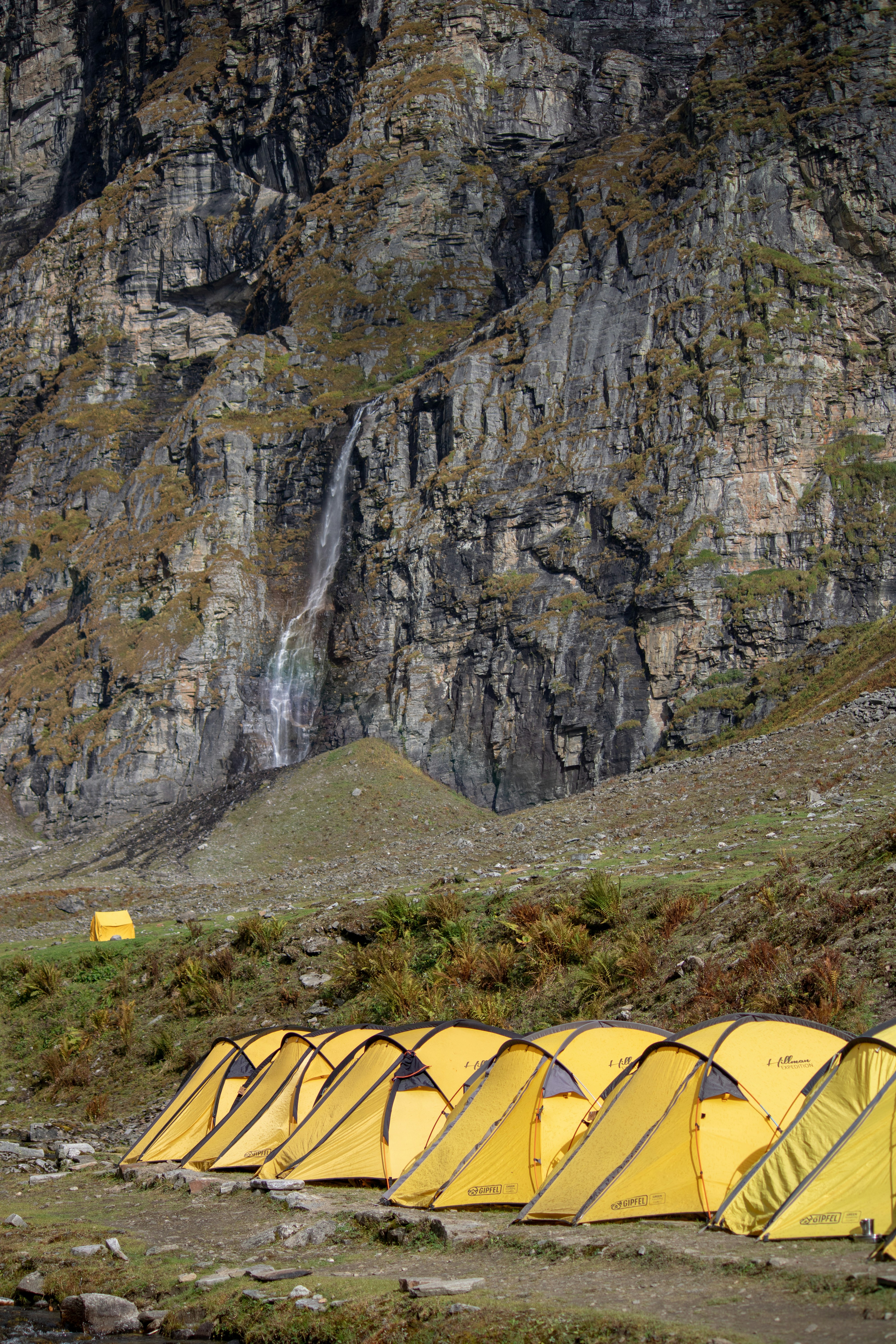 Yellow camping tents nestled in a rugged landscape with a cascading waterfall in the background.