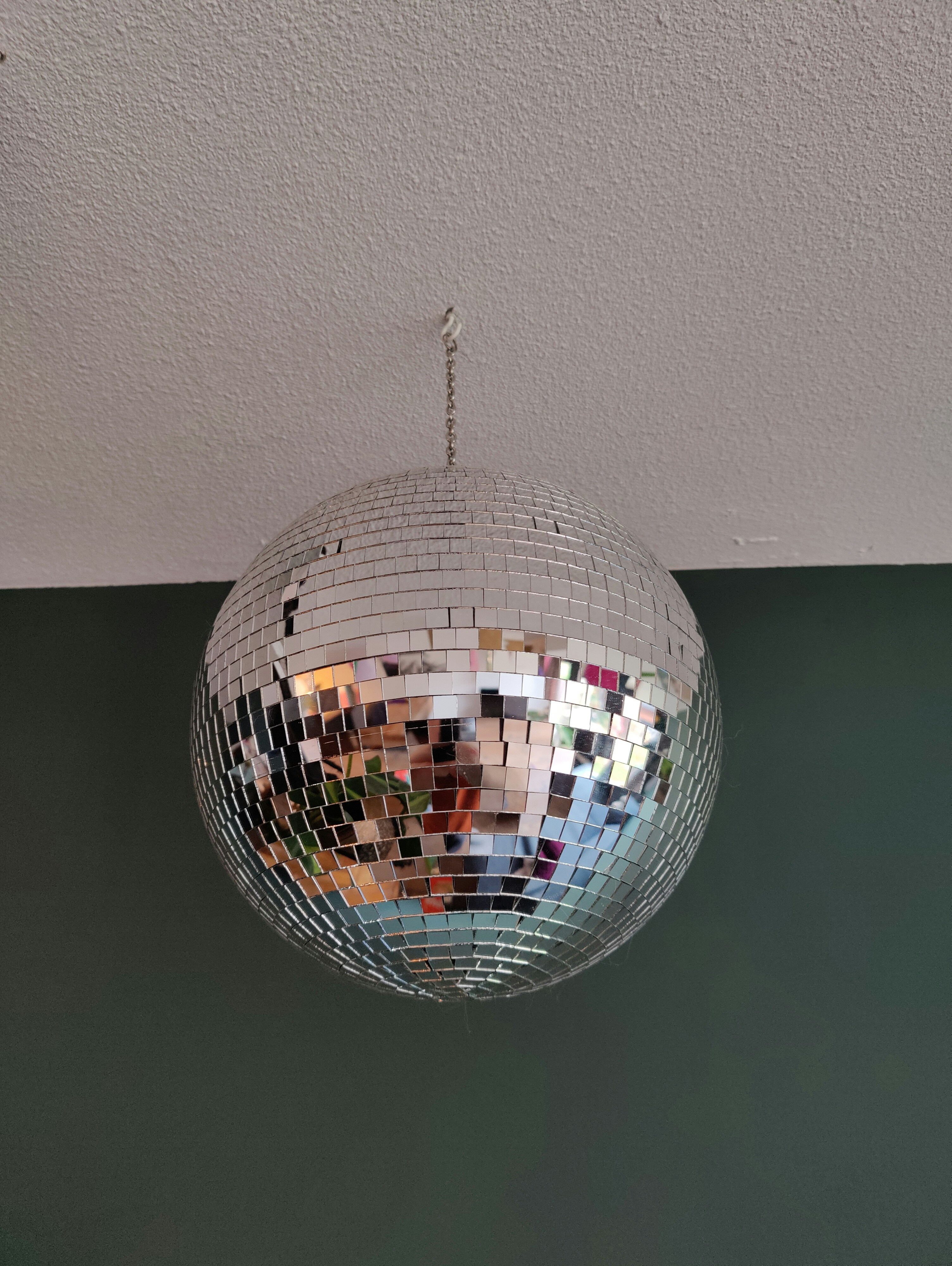 A shimmering disco ball suspended from the ceiling, reflecting vibrant colors onto a dark green wall.