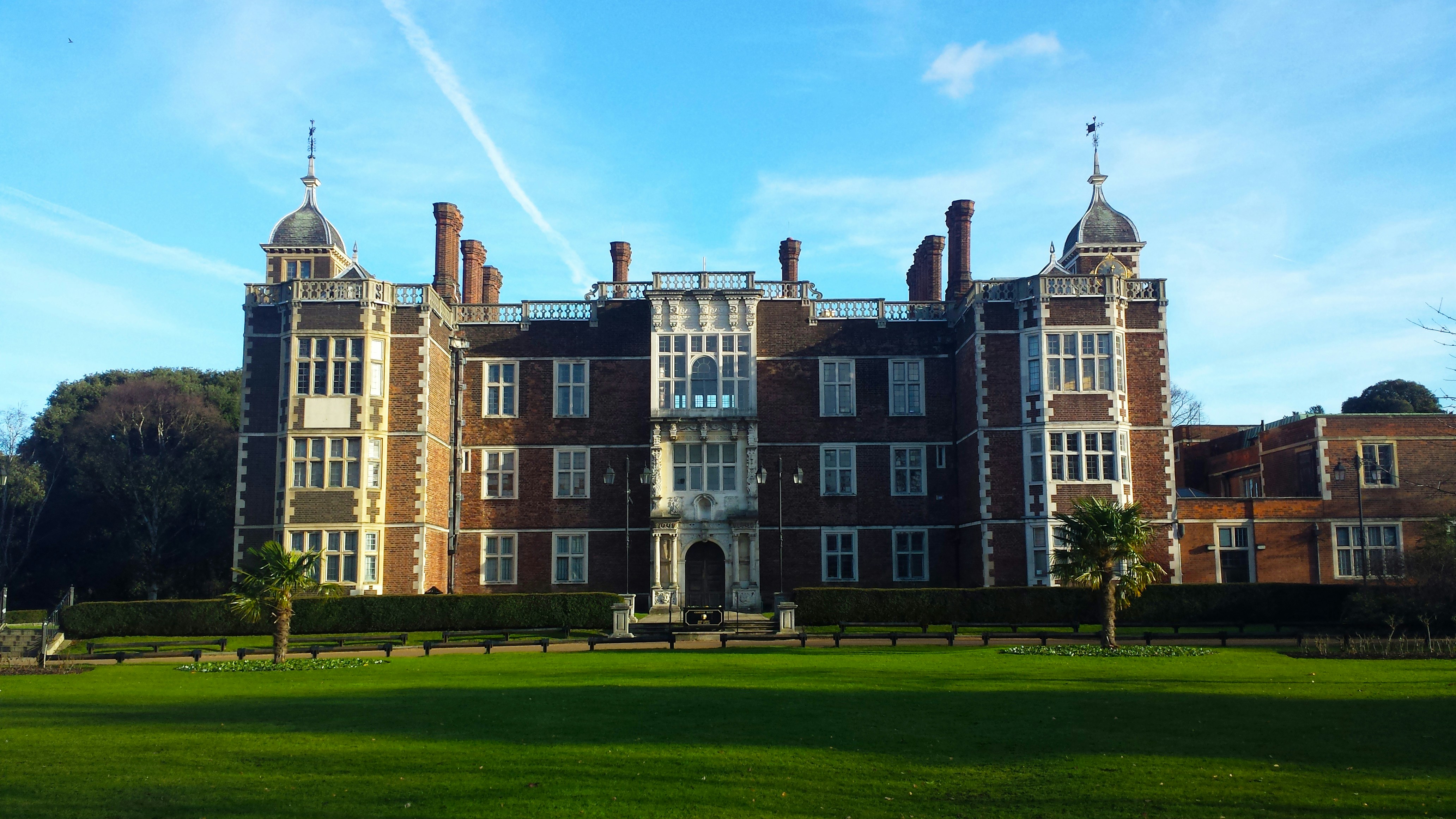 Charlton House's symmetrical architecture framed by lush greenery and a vibrant blue sky.