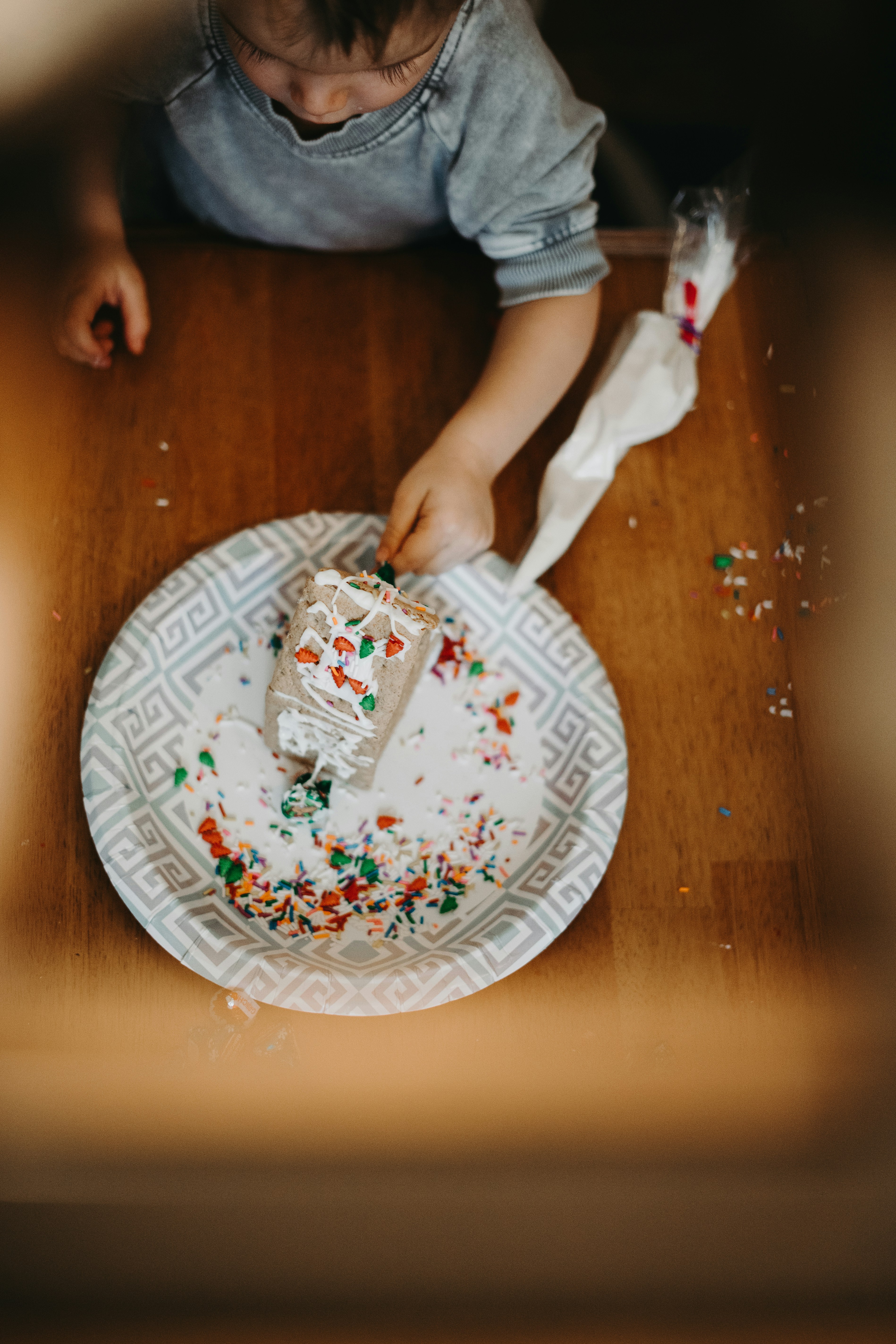 Child decorating a dessert with colorful sprinkles and frosting on a patterned plate.