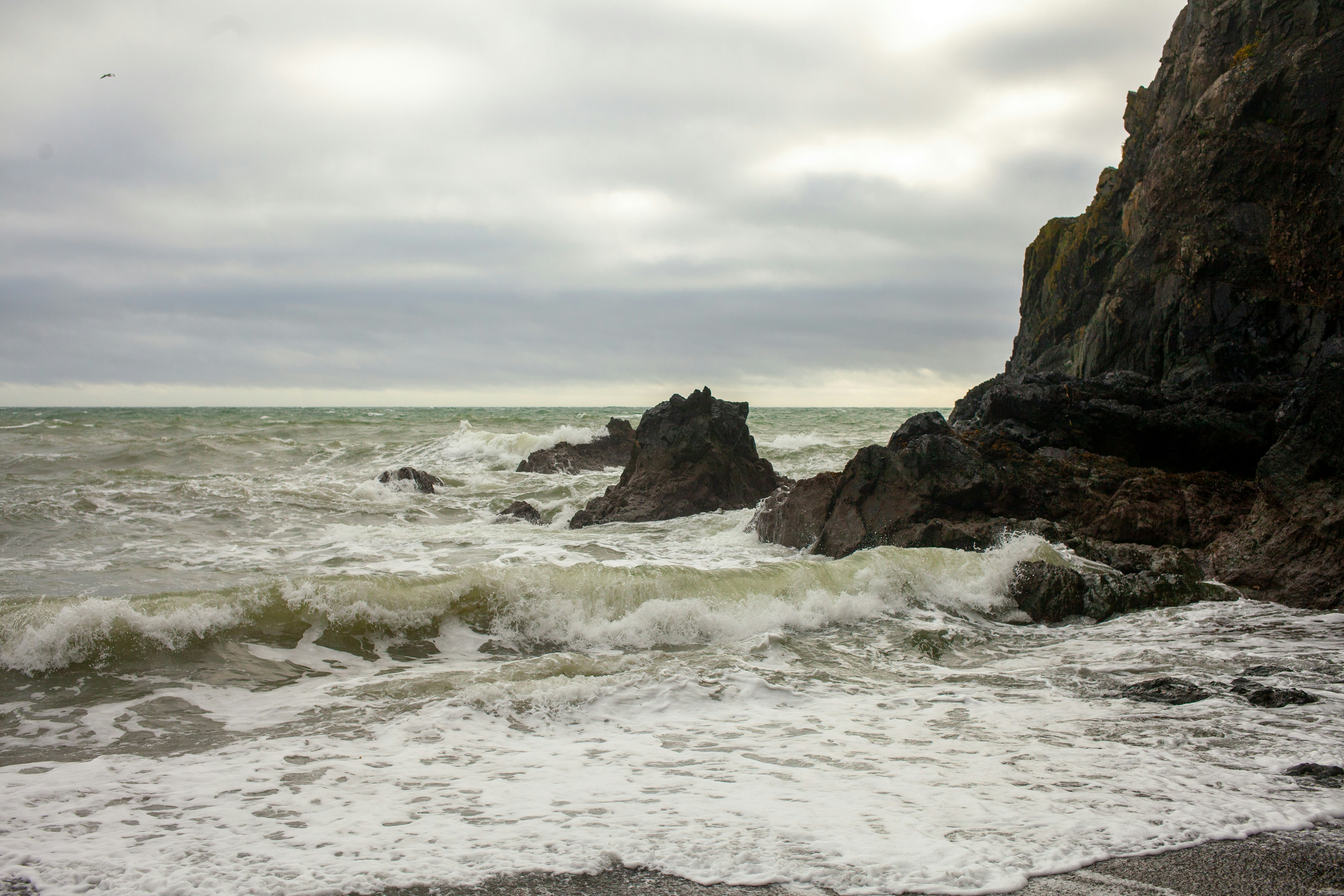 Waves crashing against rocky cliffs under a cloudy sky.