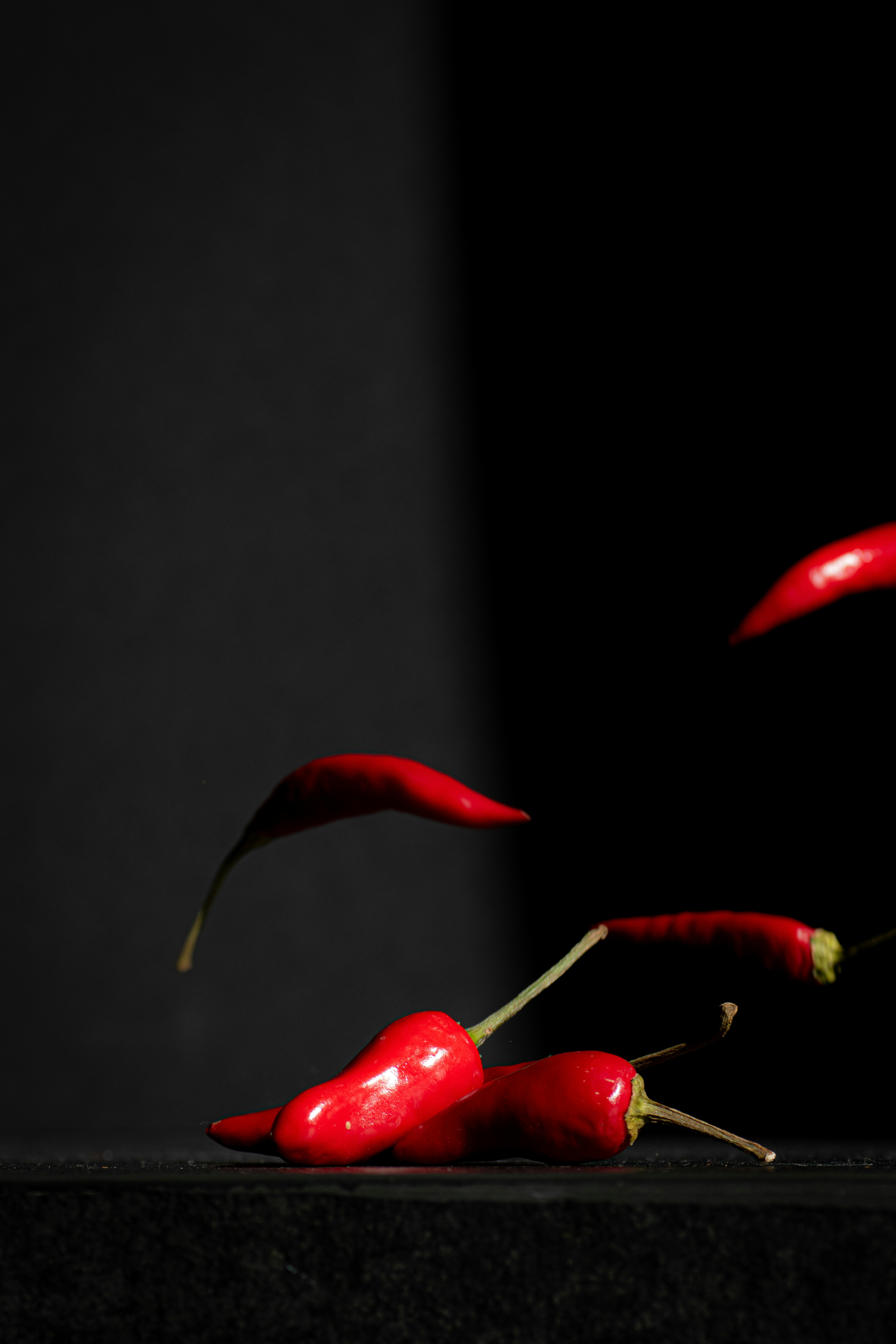 A collection of vibrant red chillies suspended in mid-air against a dark backdrop, emphasizing their vivid color and dynamic movement.