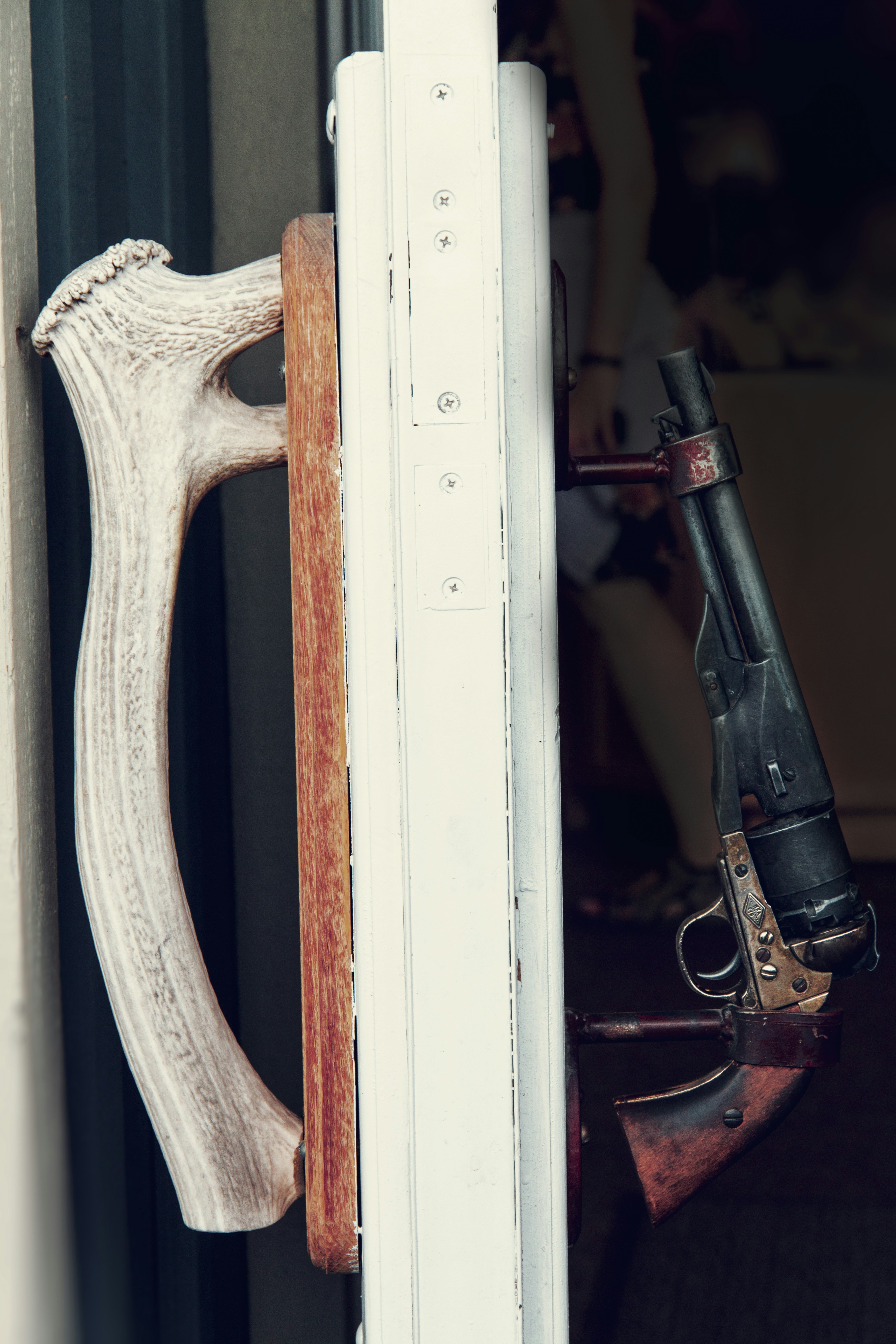 A rustic door handle crafted from antlers juxtaposed with a vintage revolver, symbolizing the blend of nature and human craftsmanship.