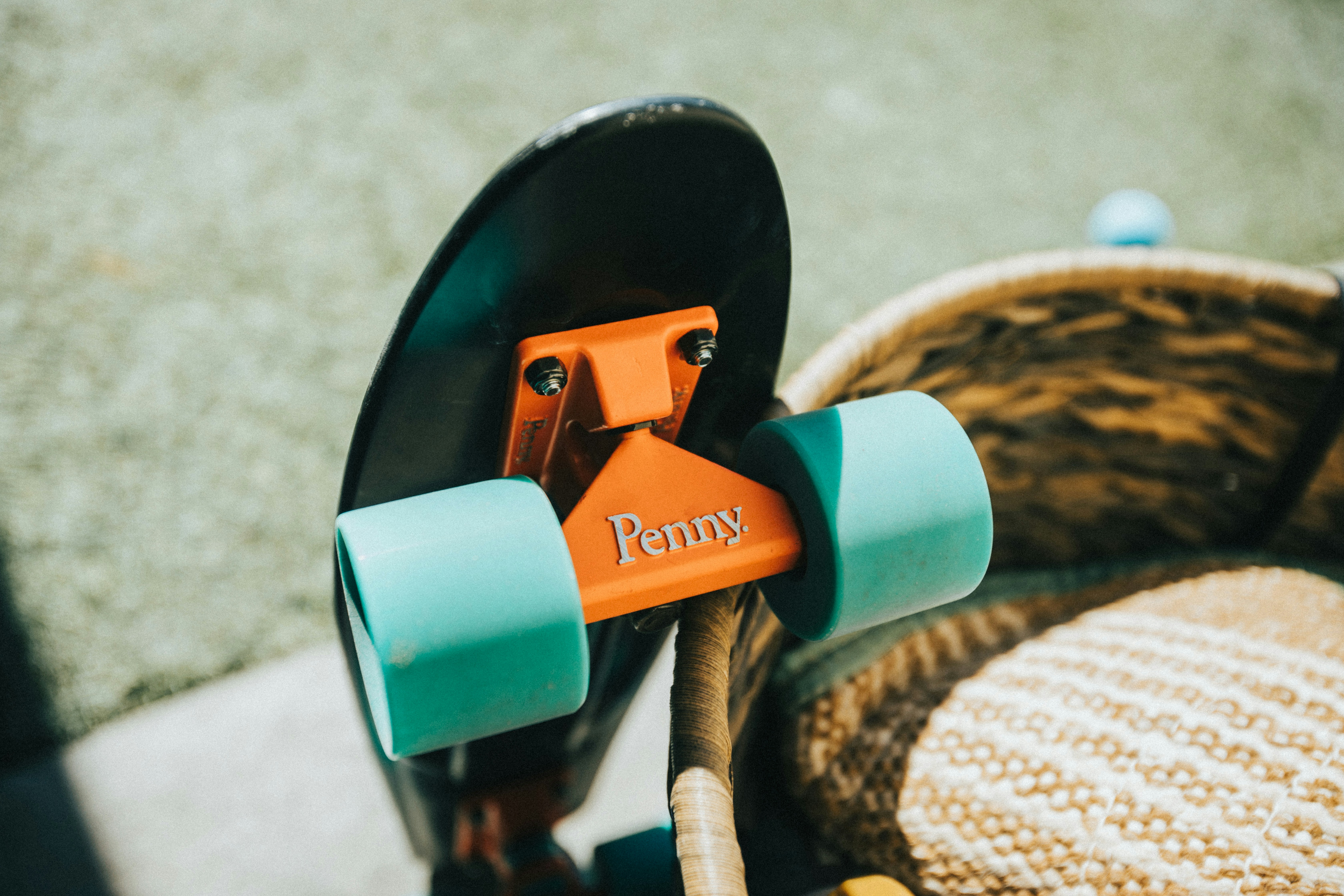 Close-up of a vibrant Penny skateboard resting against a woven chair, showcasing its colorful wheels and unique design.