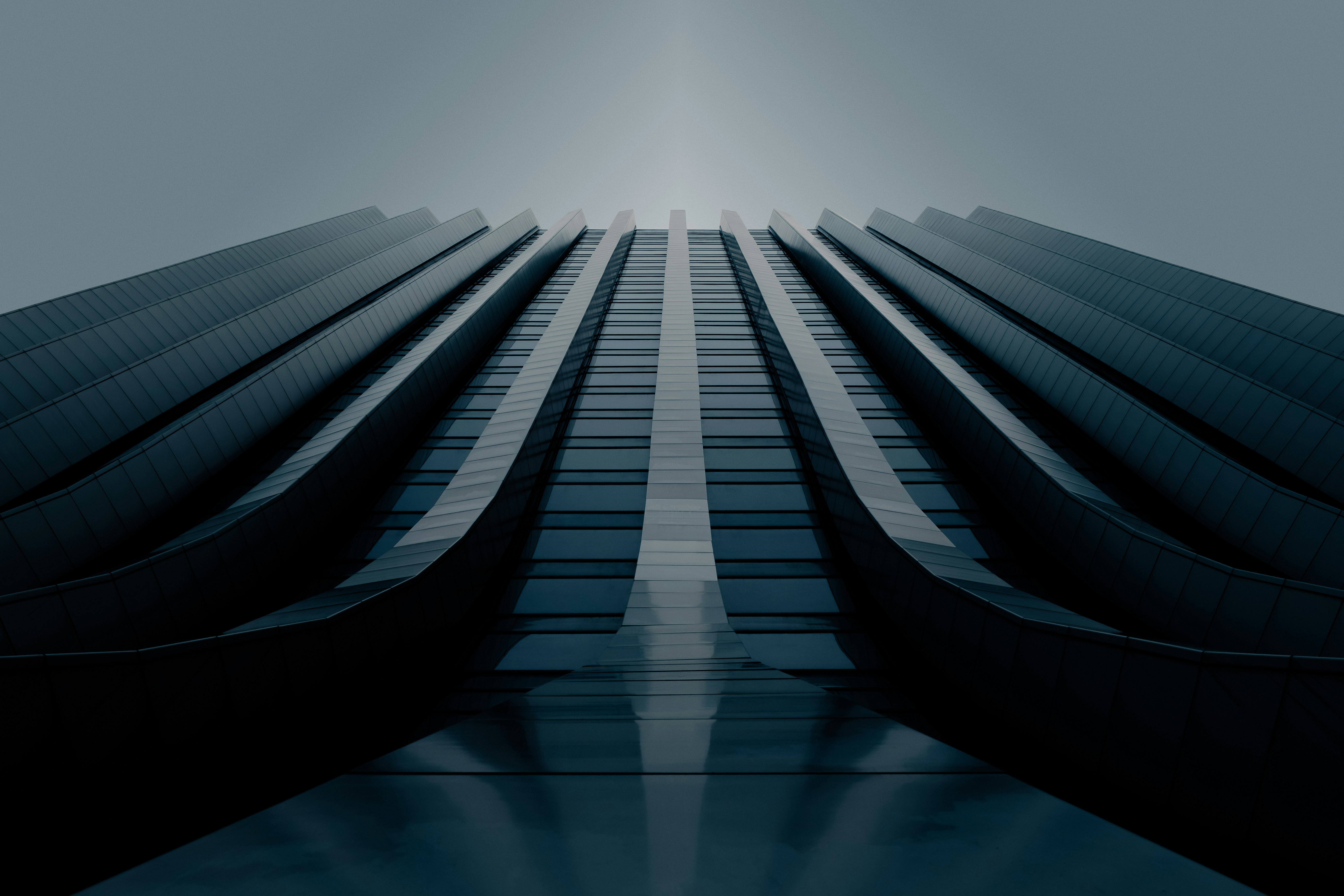 Curving aluminum fins and glass facade of a skyscraper against a muted sky.