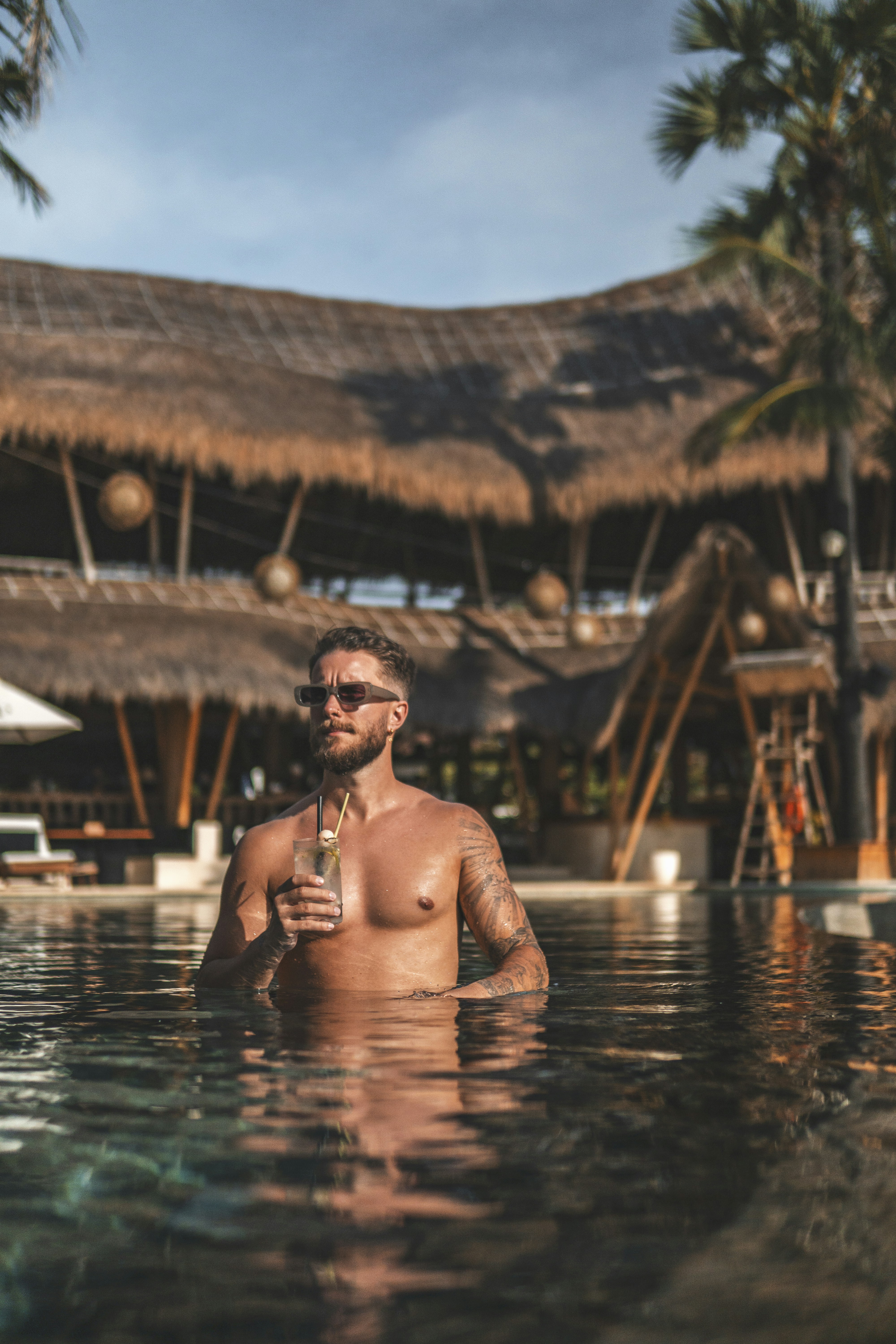 a man standing in a pool holding a drink