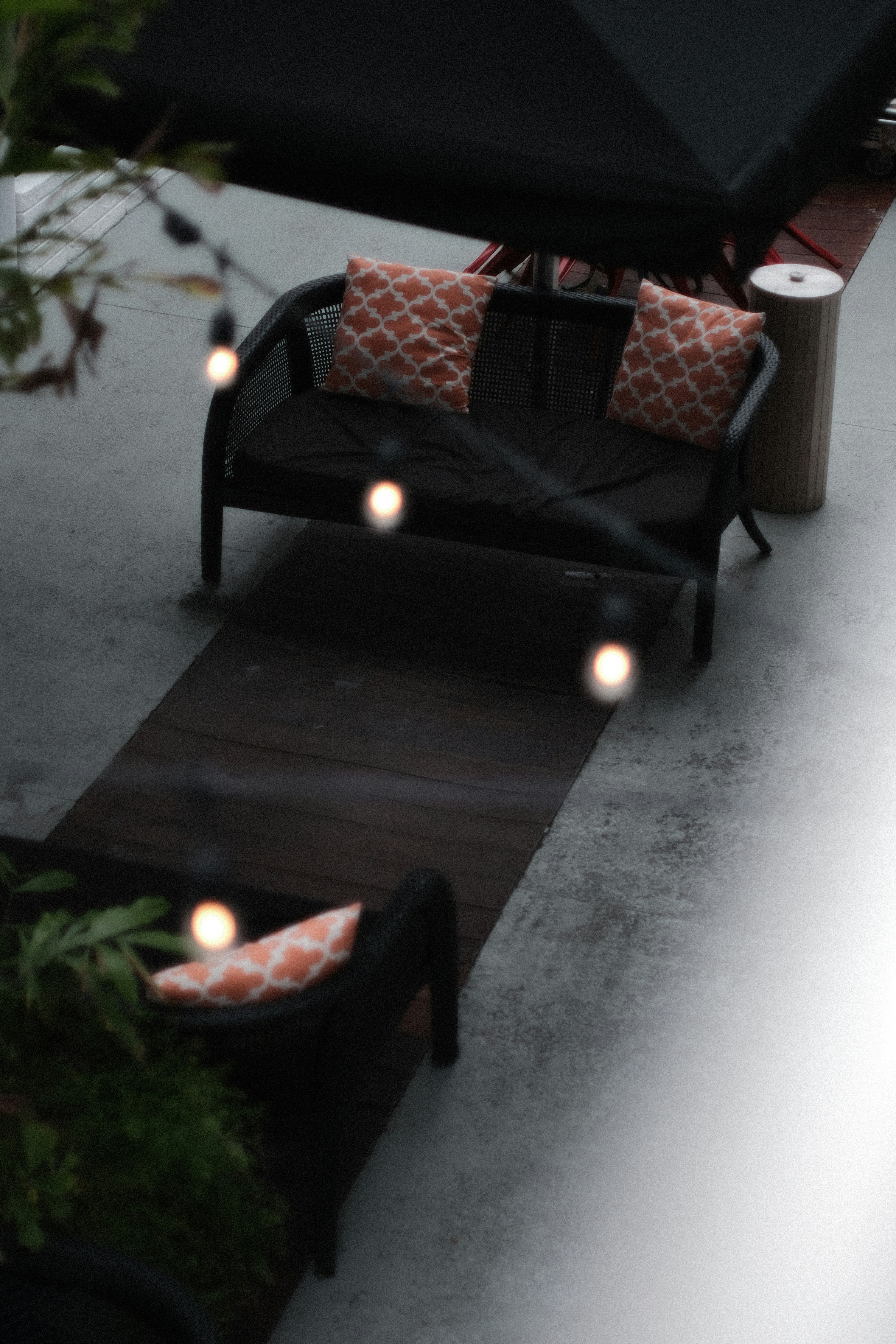 Cozy outdoor seating area featuring black wicker chairs adorned with orange cushions, illuminated by soft, glowing lights.