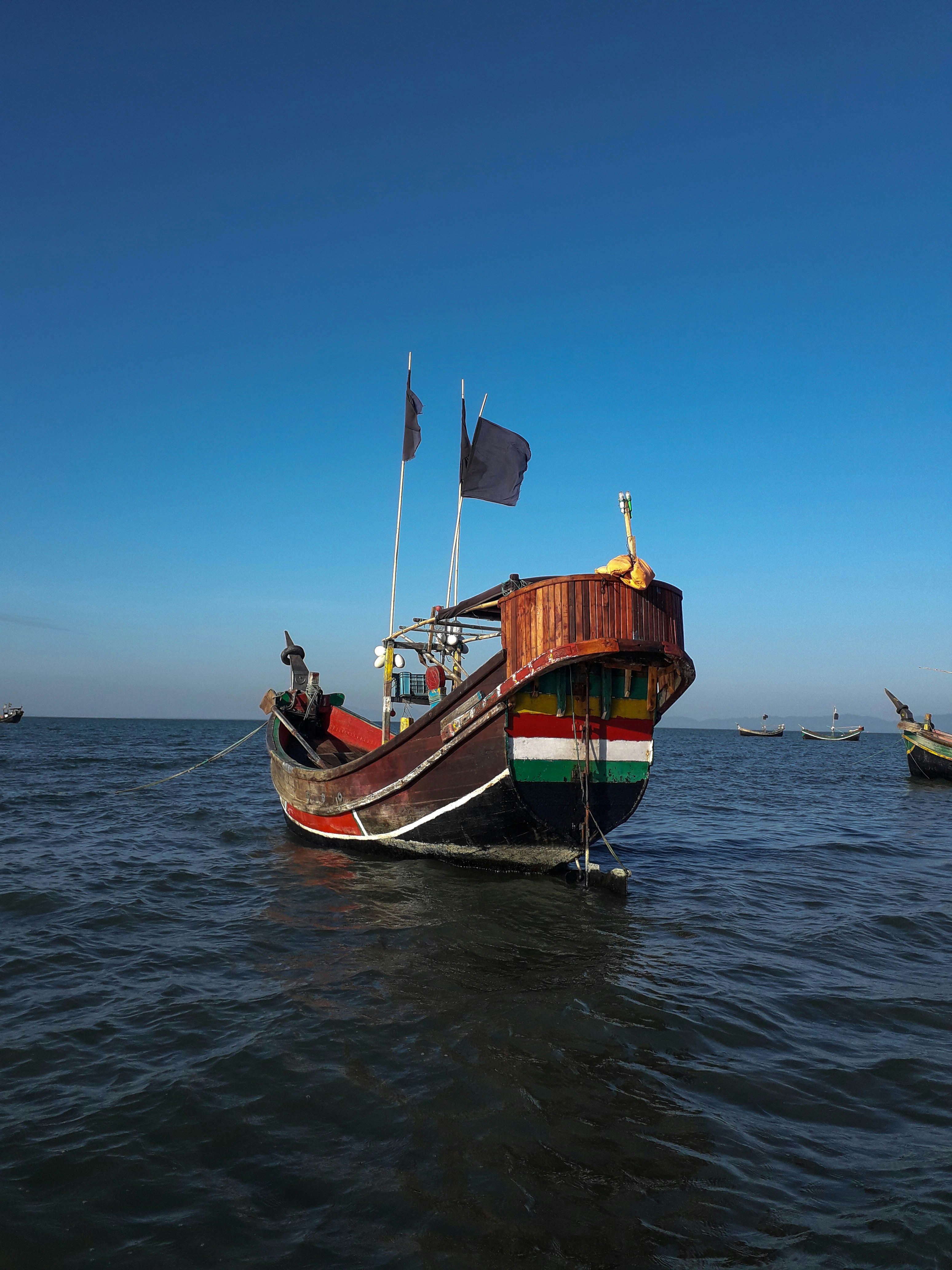 A colorful fishing boat anchored in calm waters under a clear blue sky, showcasing traditional design elements and vibrant colors.
