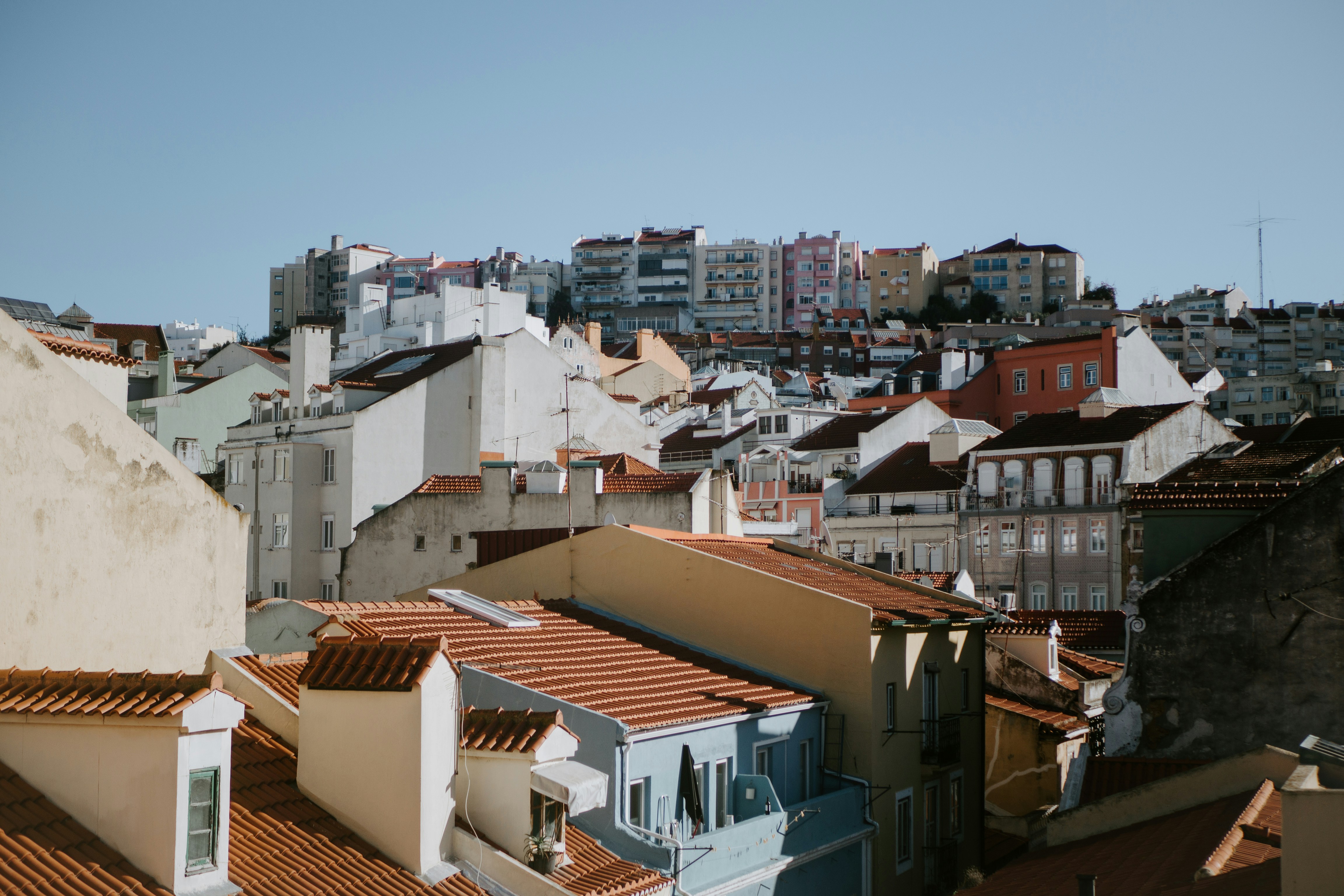 A panoramic view of colorful rooftops in a bustling urban landscape, showcasing a blend of architectural styles and terracotta tiles under a clear blue sky.
