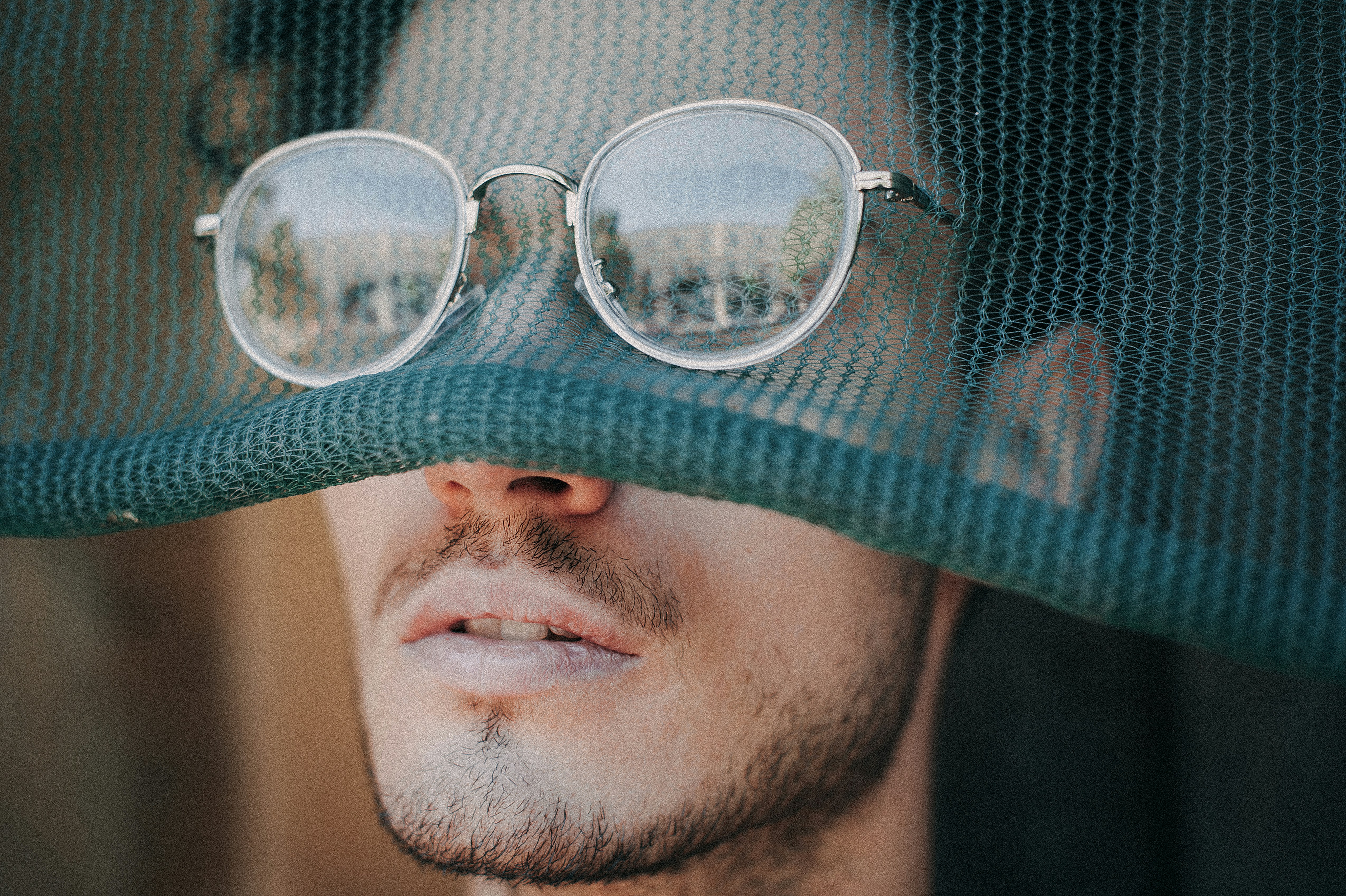 Close-up of a person with glasses partially obscured by a mesh fabric.