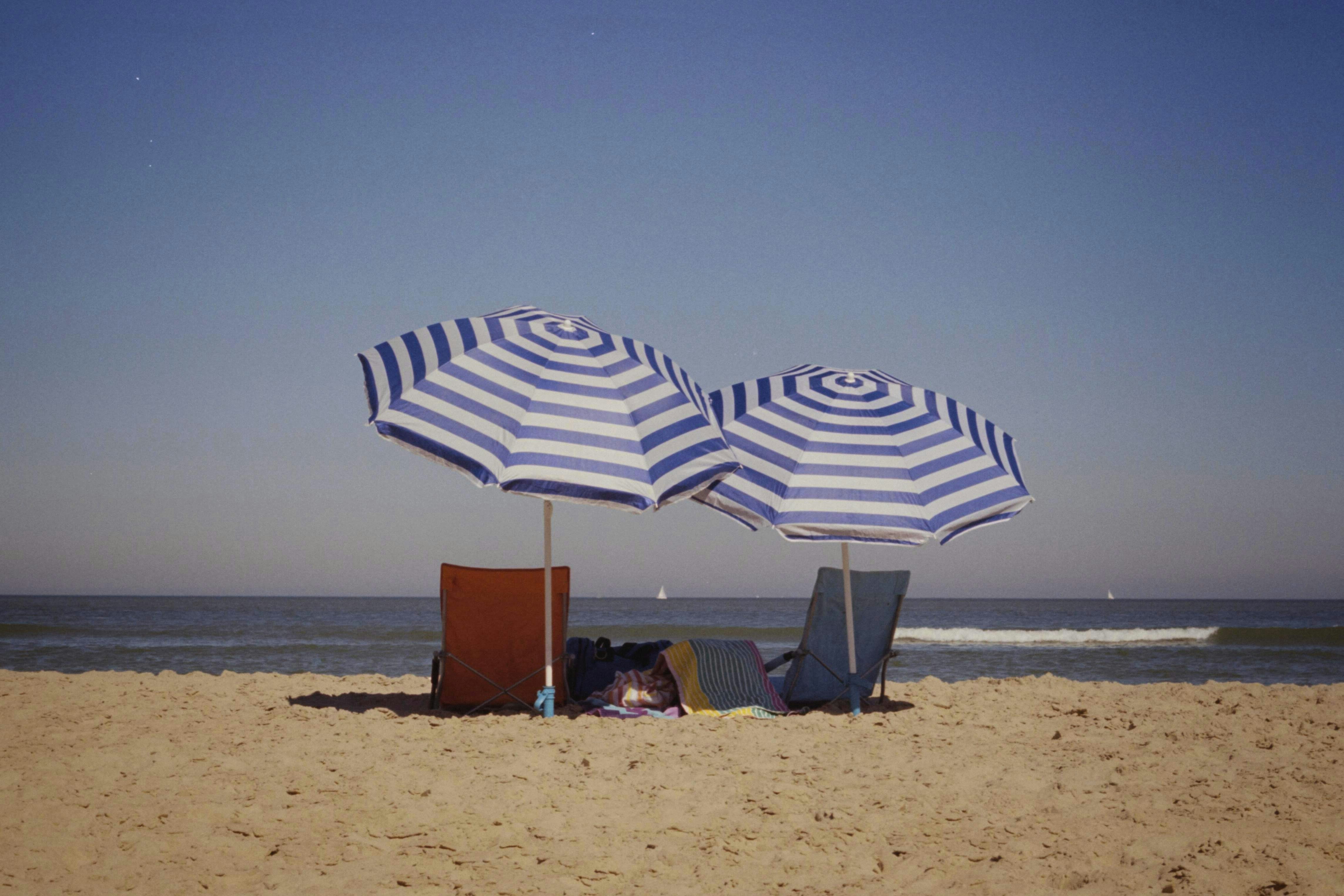 Striped beach umbrellas provide shade for sunbathers on a sandy shore, with gentle waves lapping in the background.