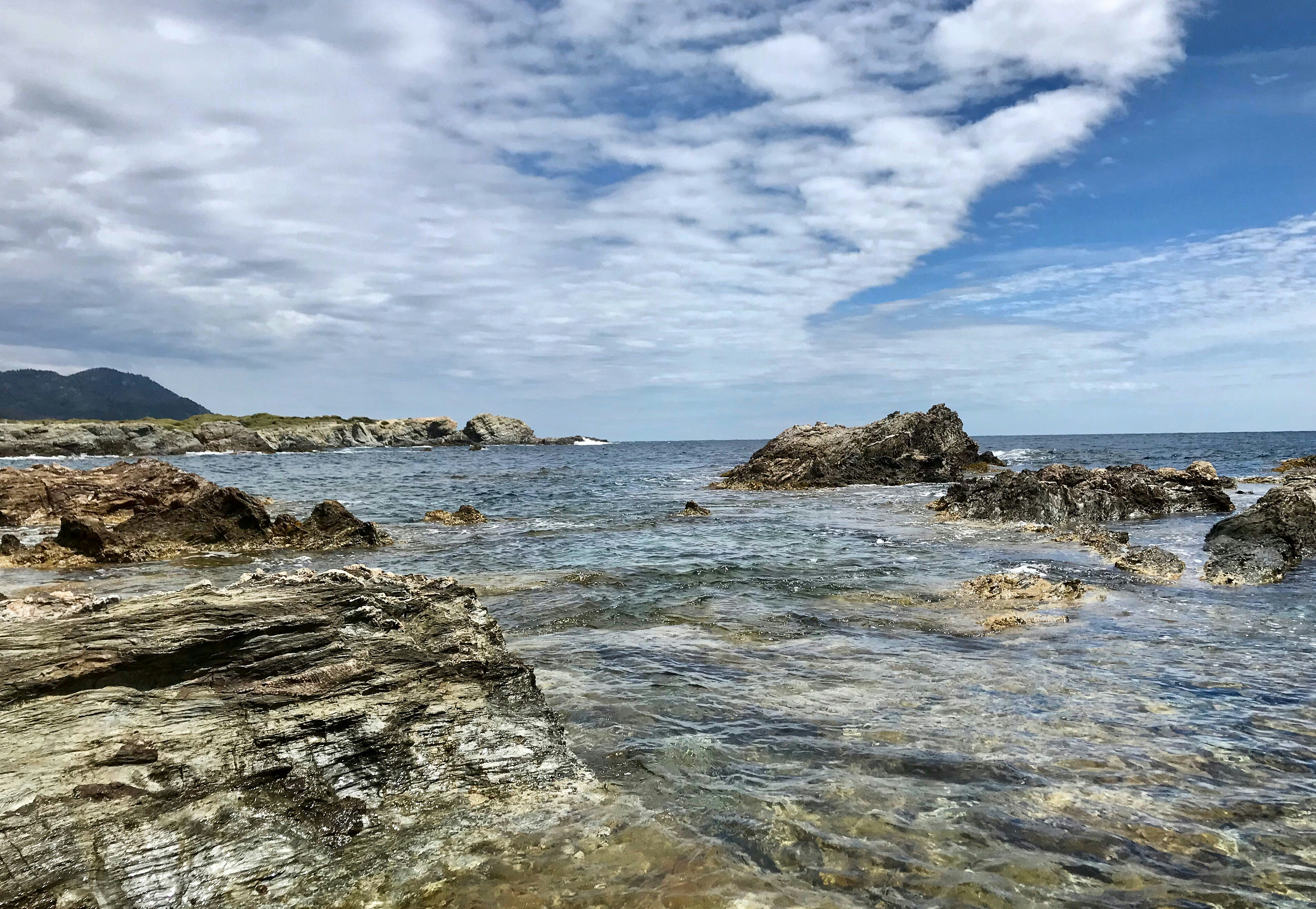 Rocky coastline with calm water beneath a partly cloudy sky.