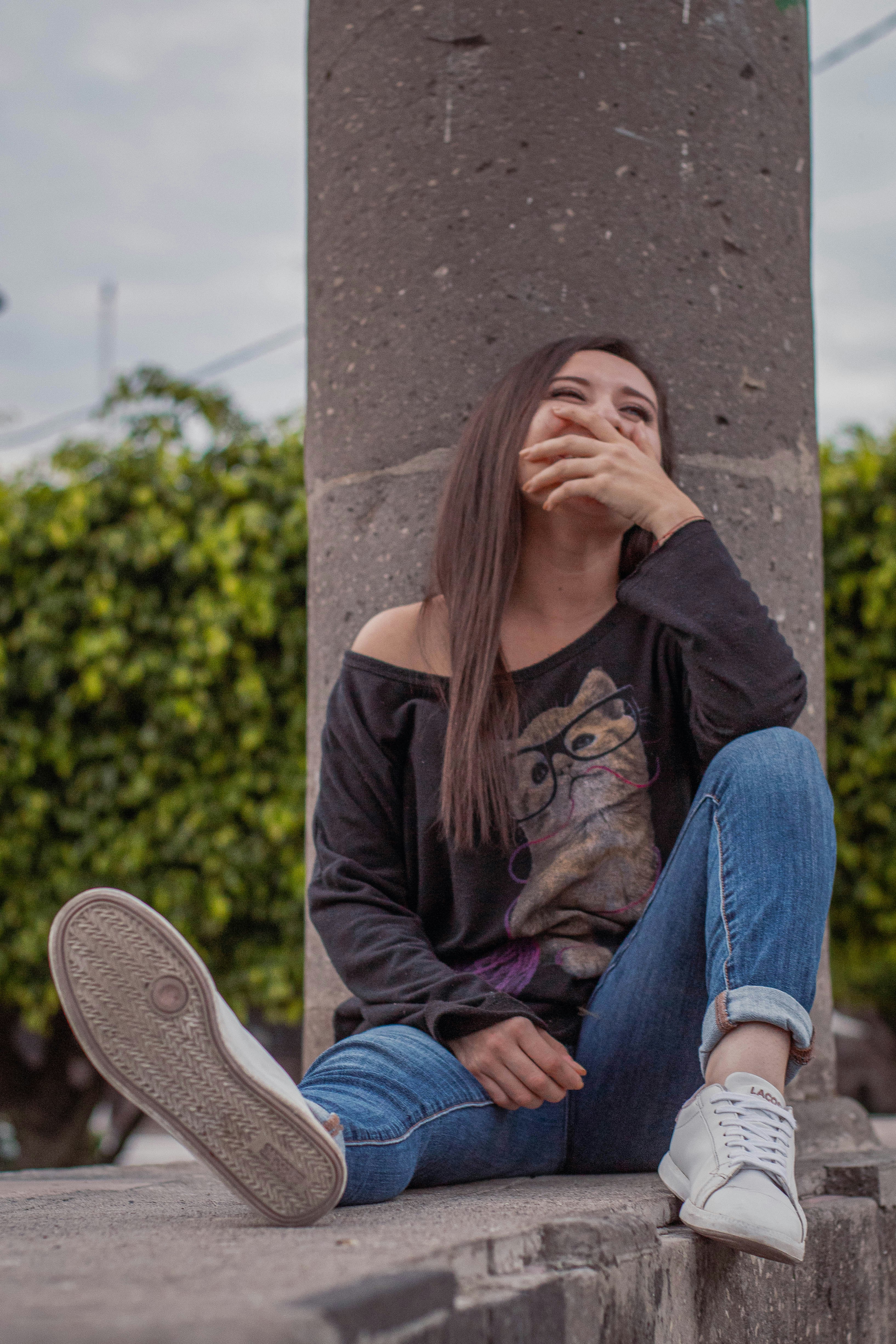 A woman sitting on a ledge with her hand on her face photo – Free Girl ...
