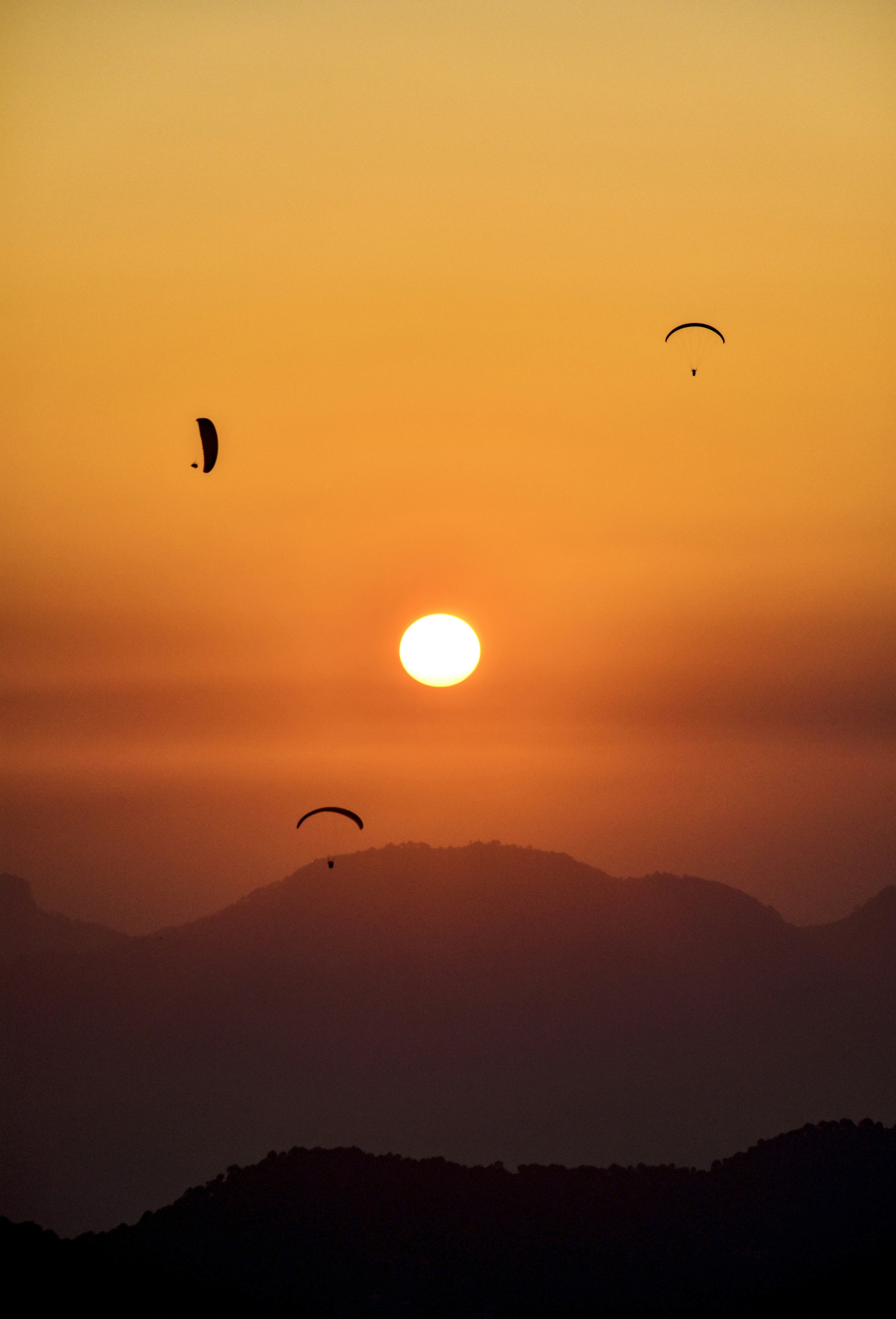 Three paragliders glide gracefully against a vibrant sunset, silhouetted against the horizon's warm hues.