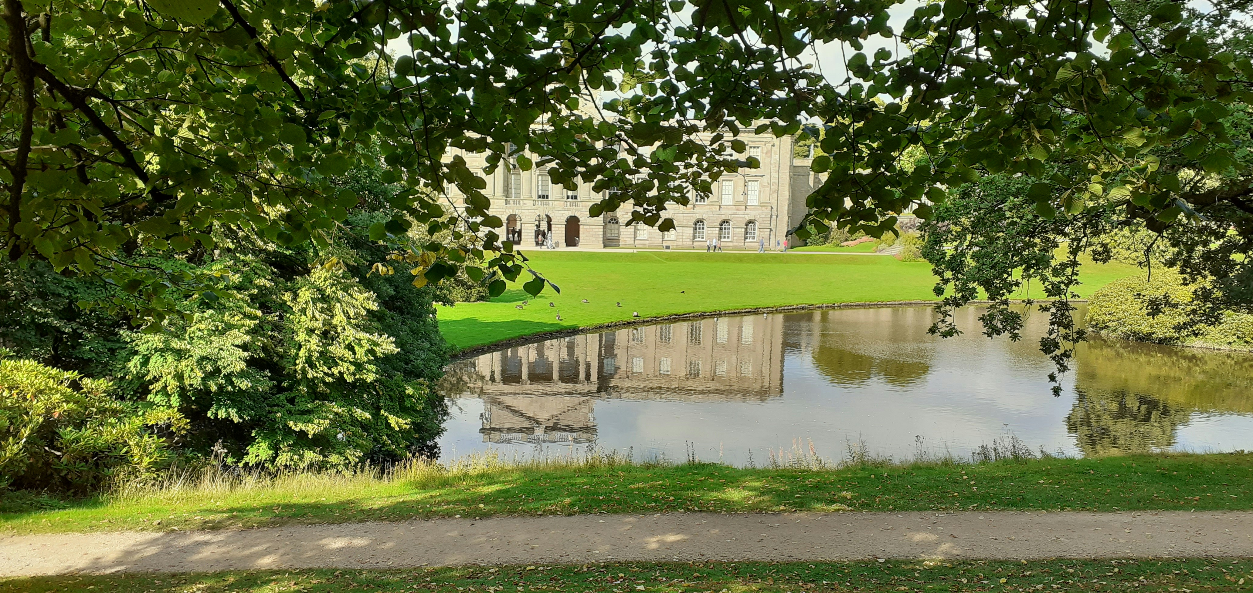 Historic manor reflected in a tranquil pond surrounded by lush greenery.