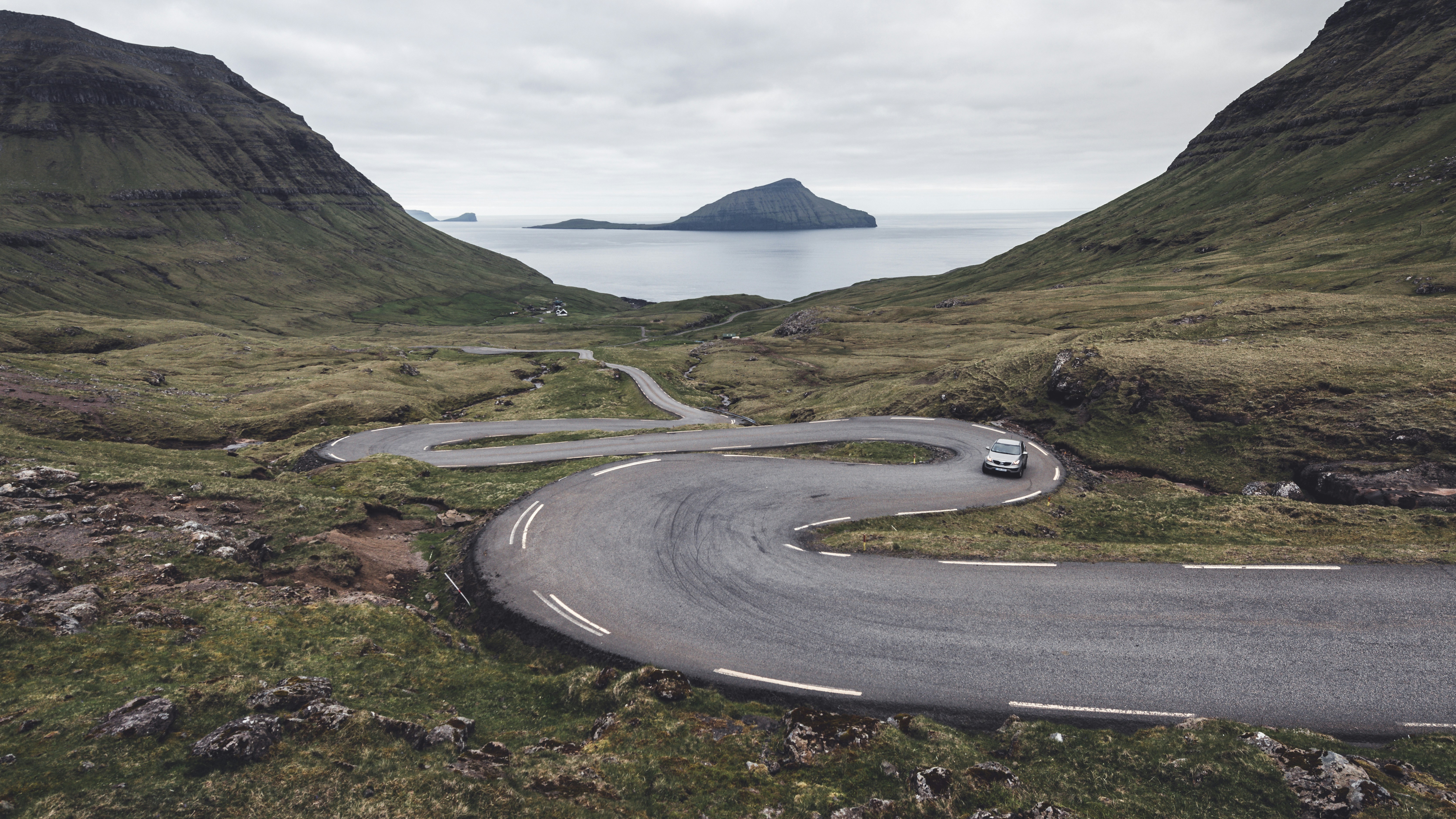 Curved mountain road leading to a serene ocean view under a cloudy sky.