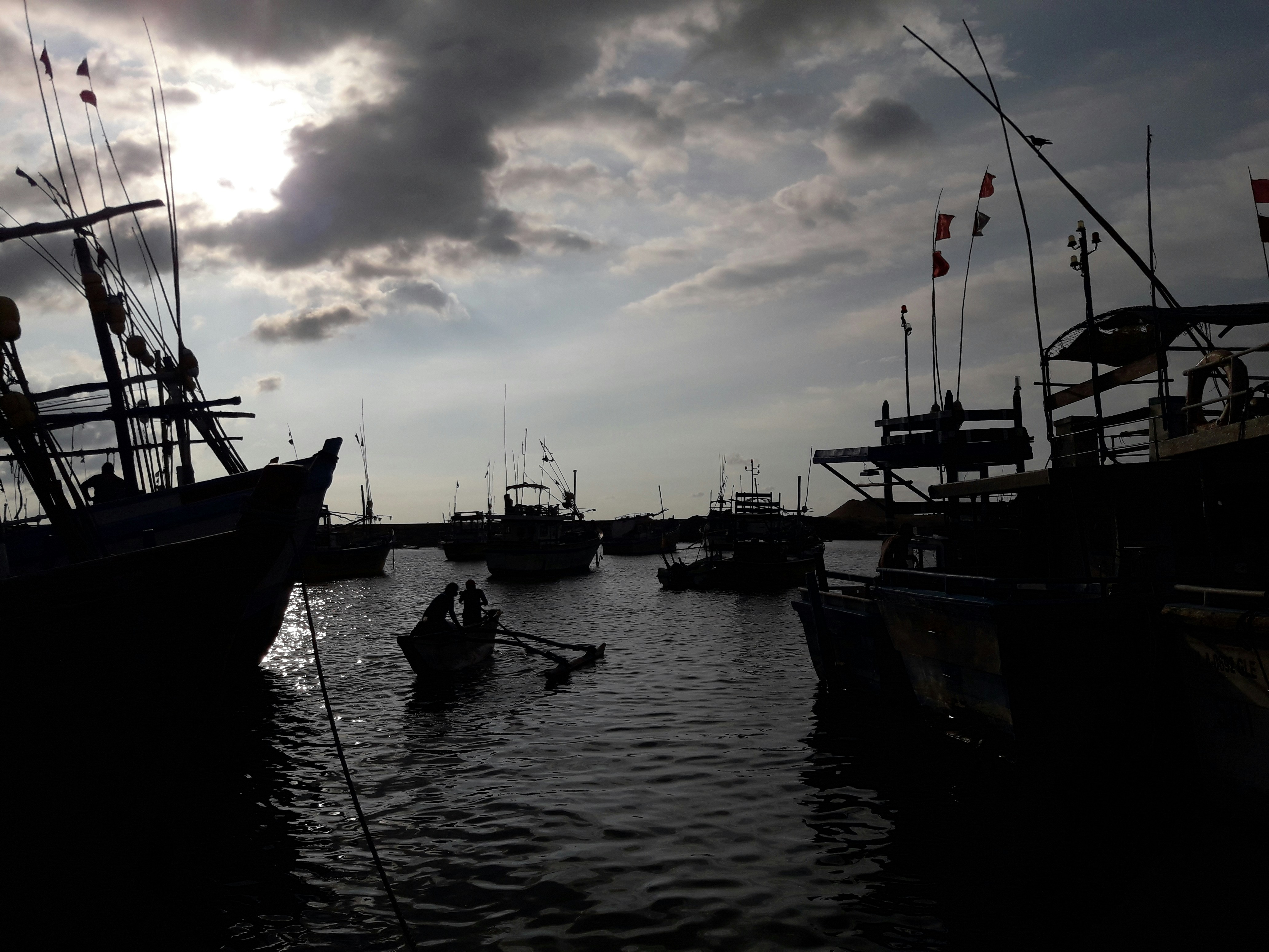 Fishing boats silhouetted against a cloudy twilight sky, creating a serene harbor scene. Flags flutter gently in the background.
