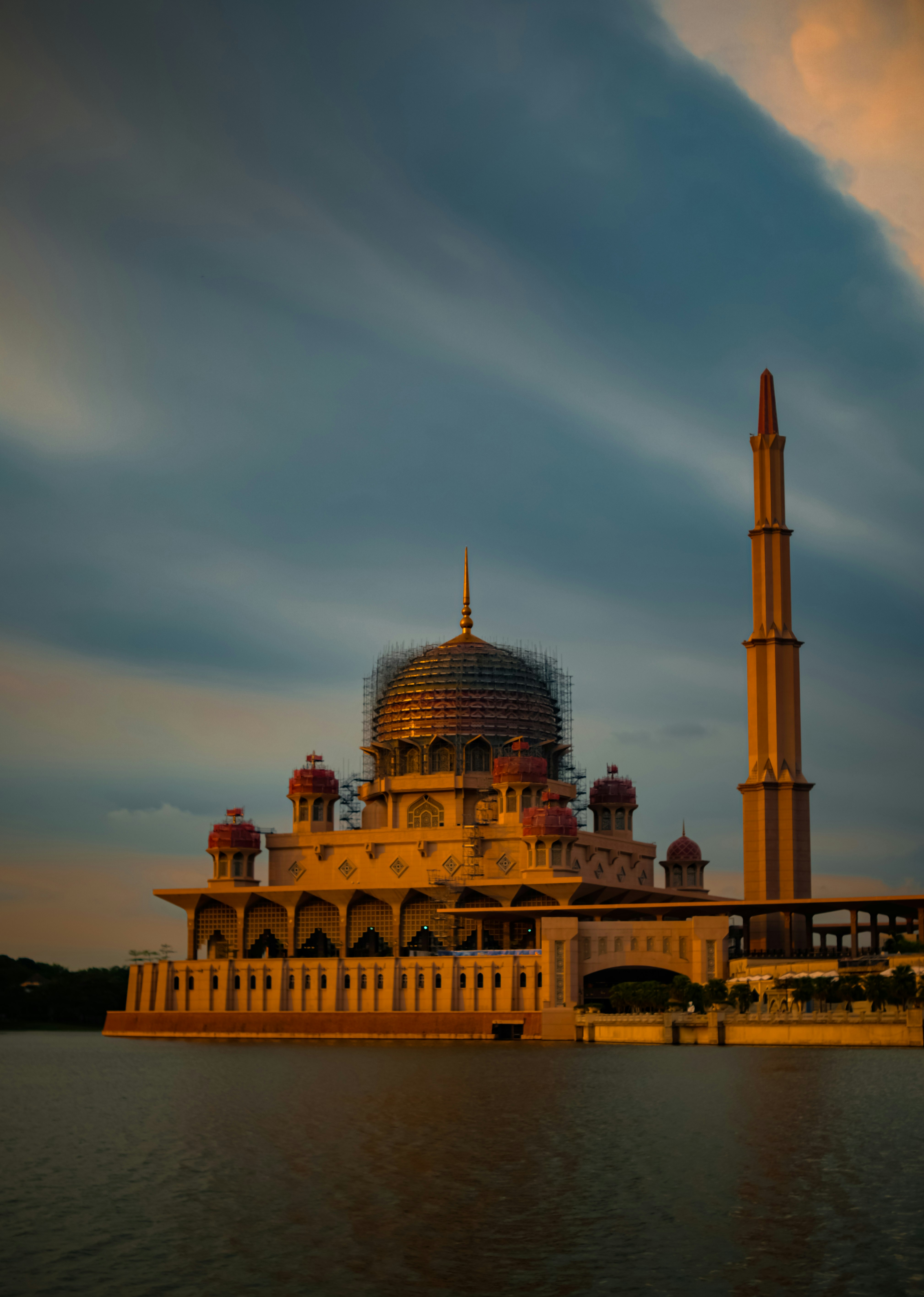 Majestic mosque with intricate domes and minarets reflecting in calm waters under a dramatic sky.
