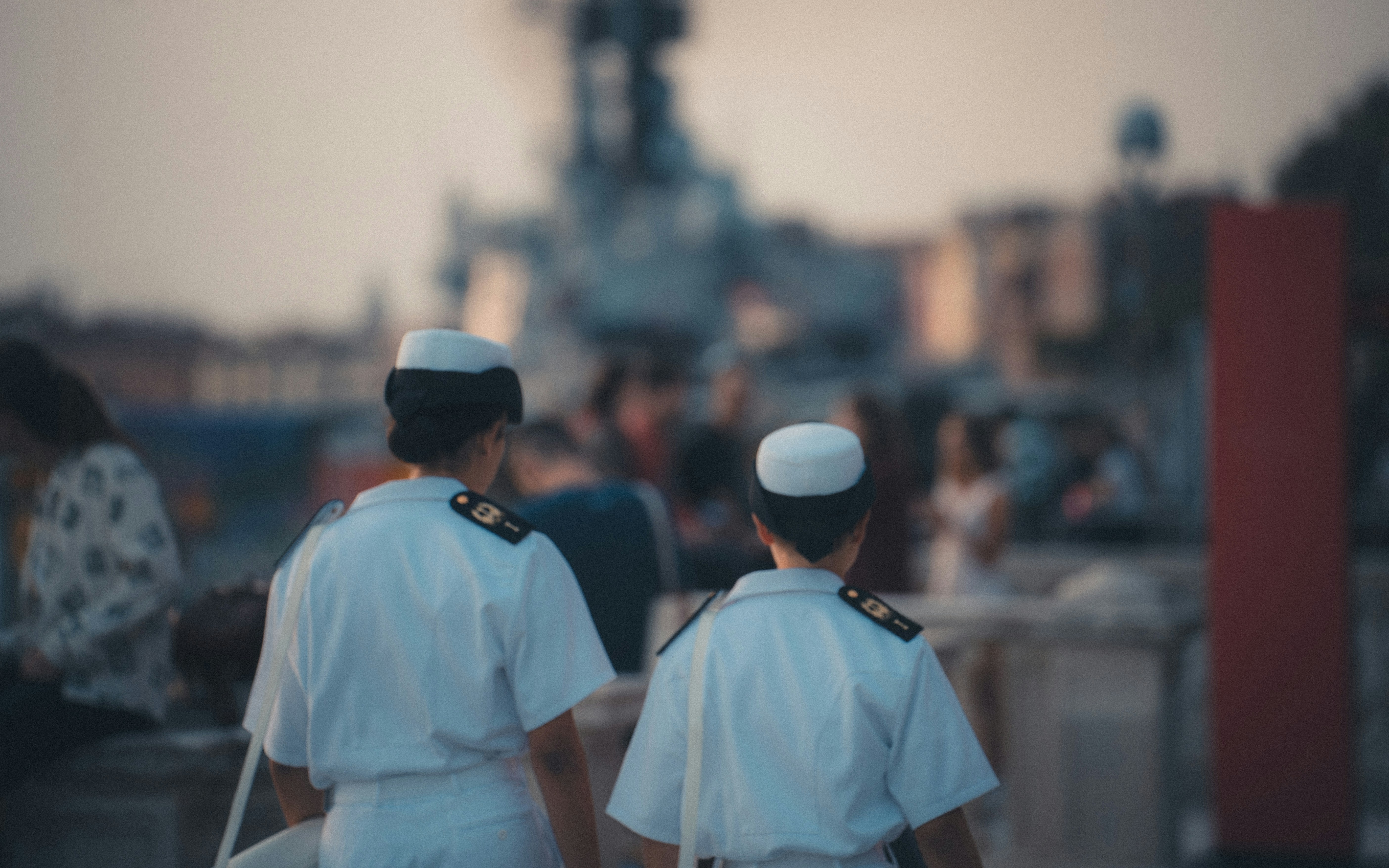 Two Sailors in White: Quiet Crossing Beneath a Distant Warship