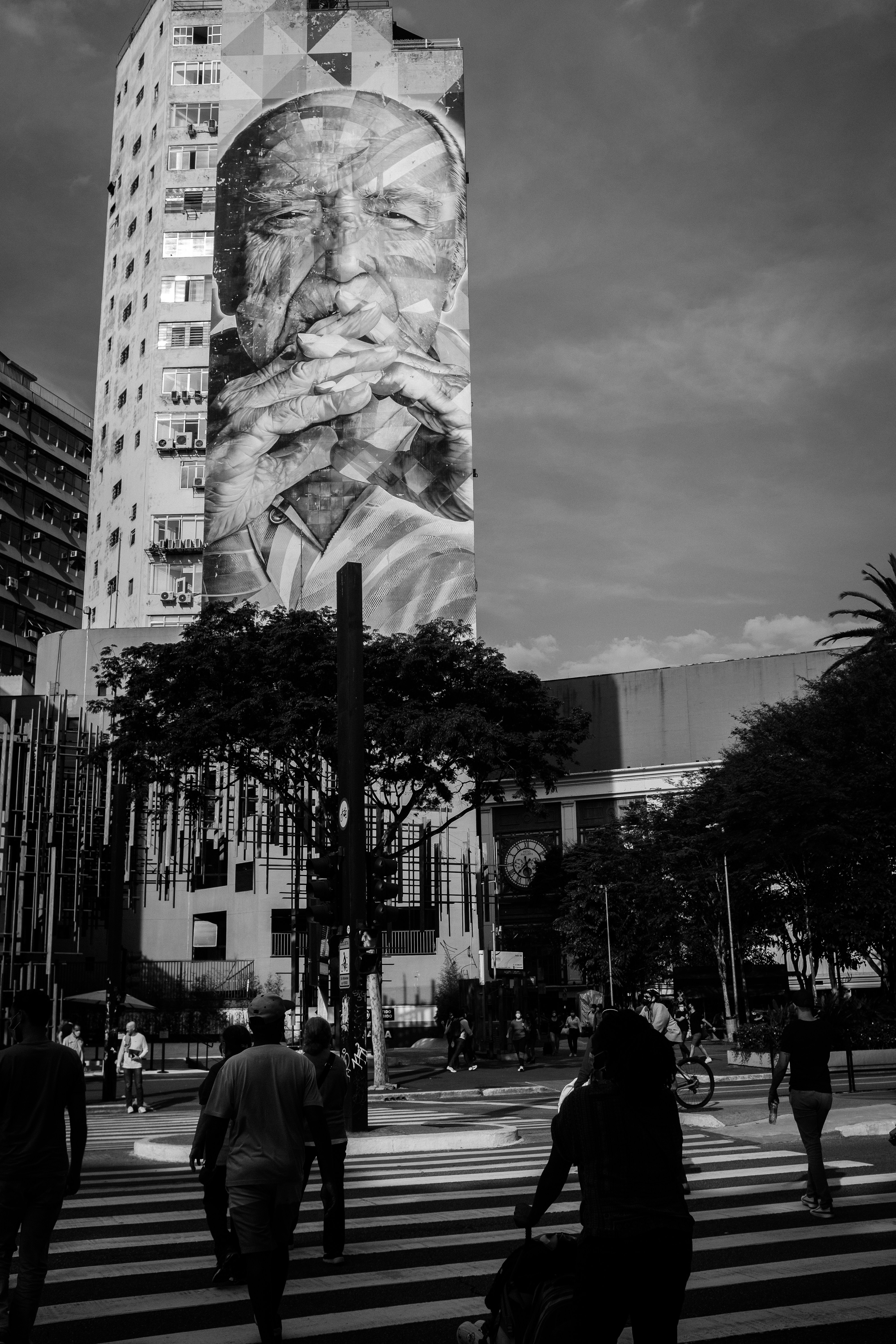 Black and white street scene with a large mural of a contemplative face on a high-rise building.