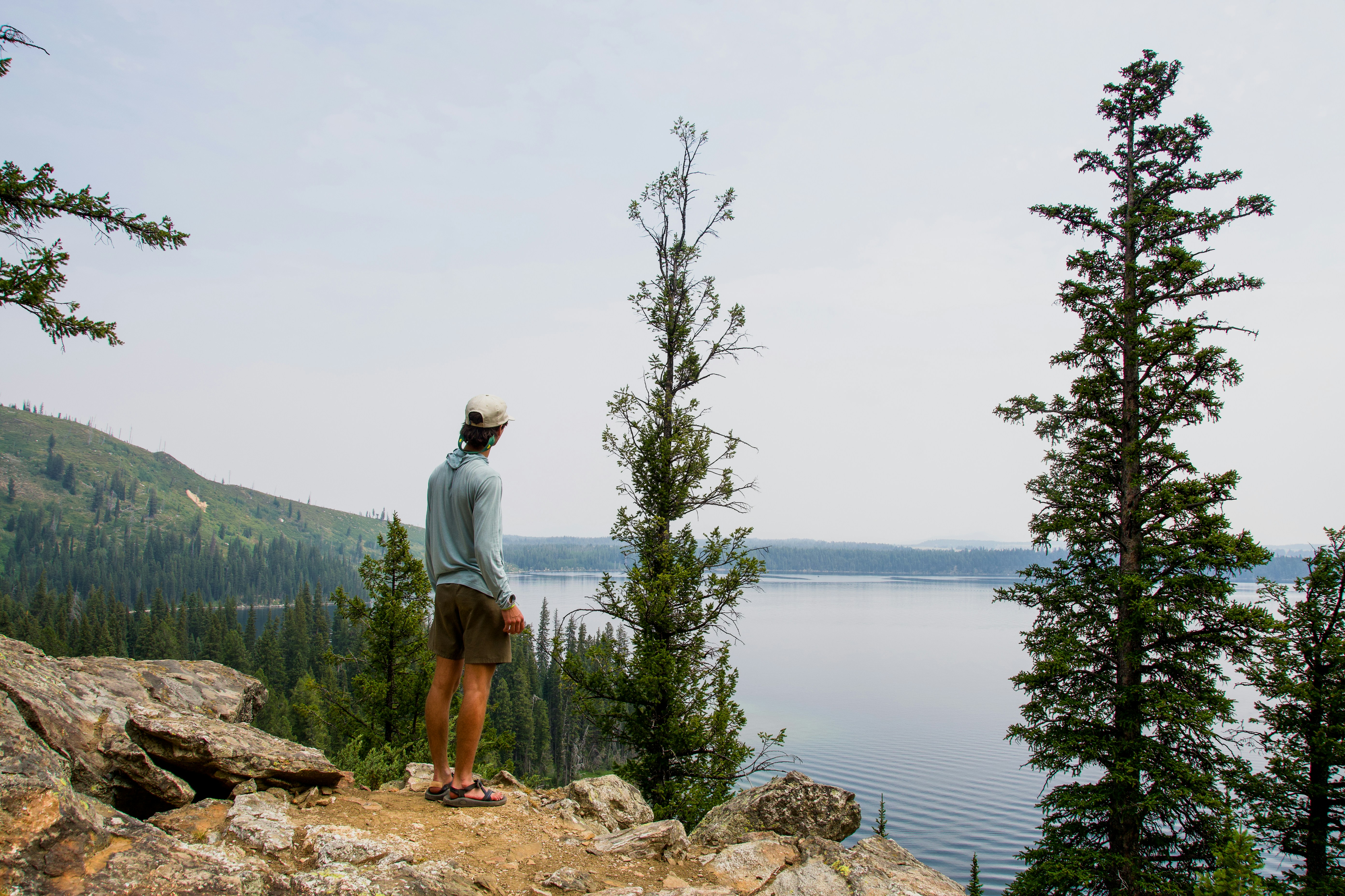 A man standing on top of a cliff overlooking a lake photo – Free Grey ...