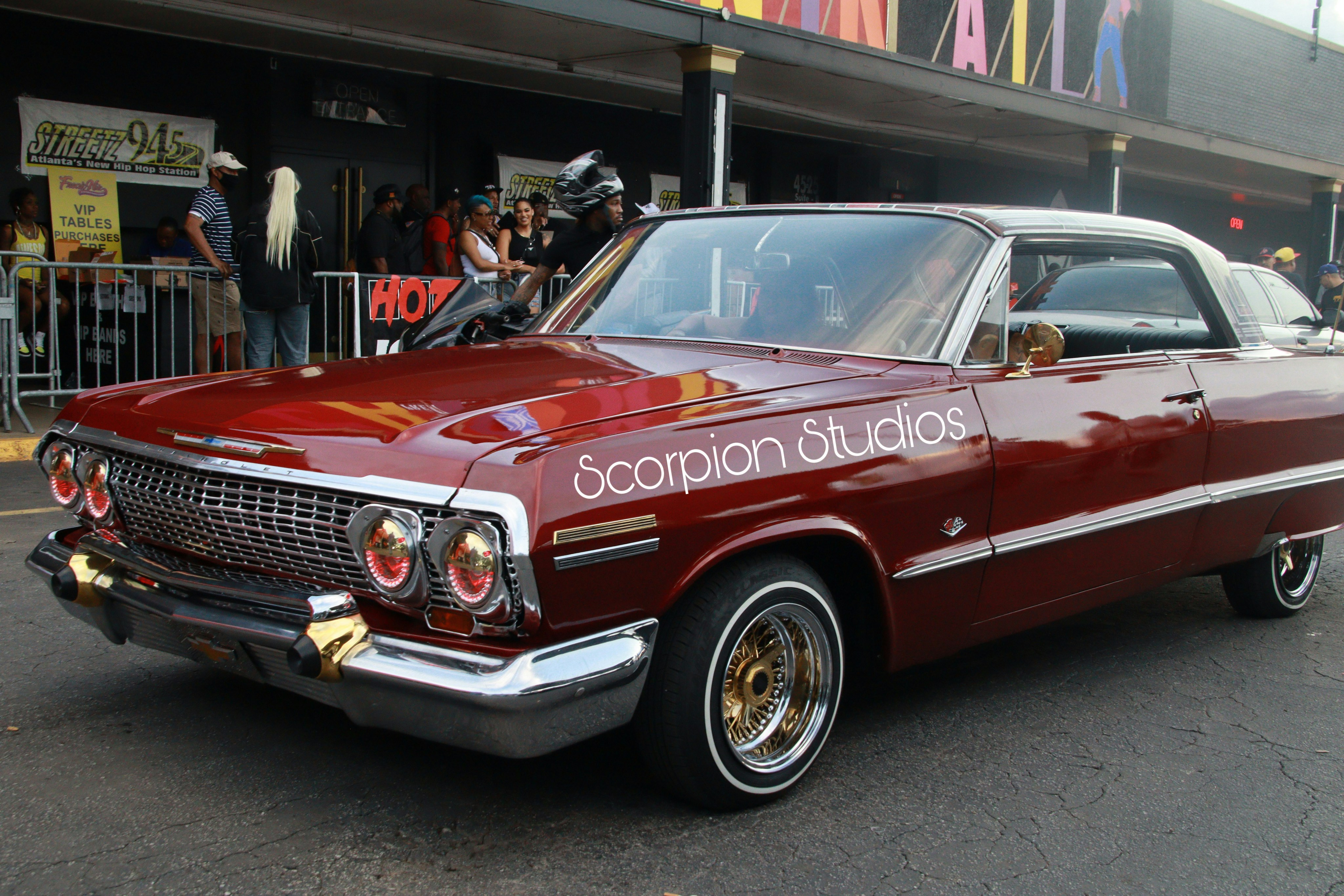 Vintage maroon car parked outside a retro studio, showcasing its polished chrome details and classic design.