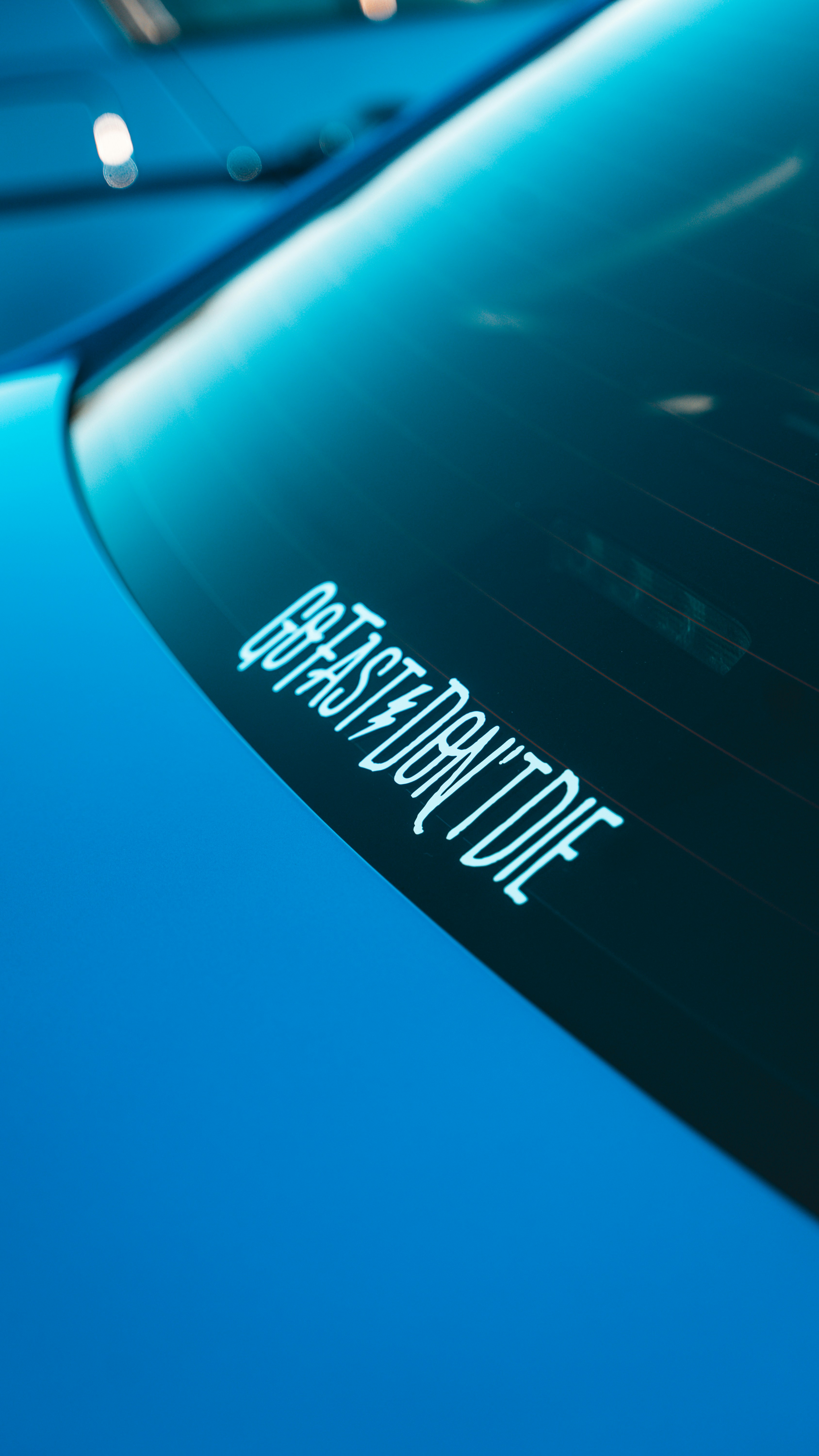 A vibrant blue car rear window adorned with a bold slogan, emphasizing a passion for speed and adrenaline. The text design adds a dynamic touch to the vehicle's aesthetic.
