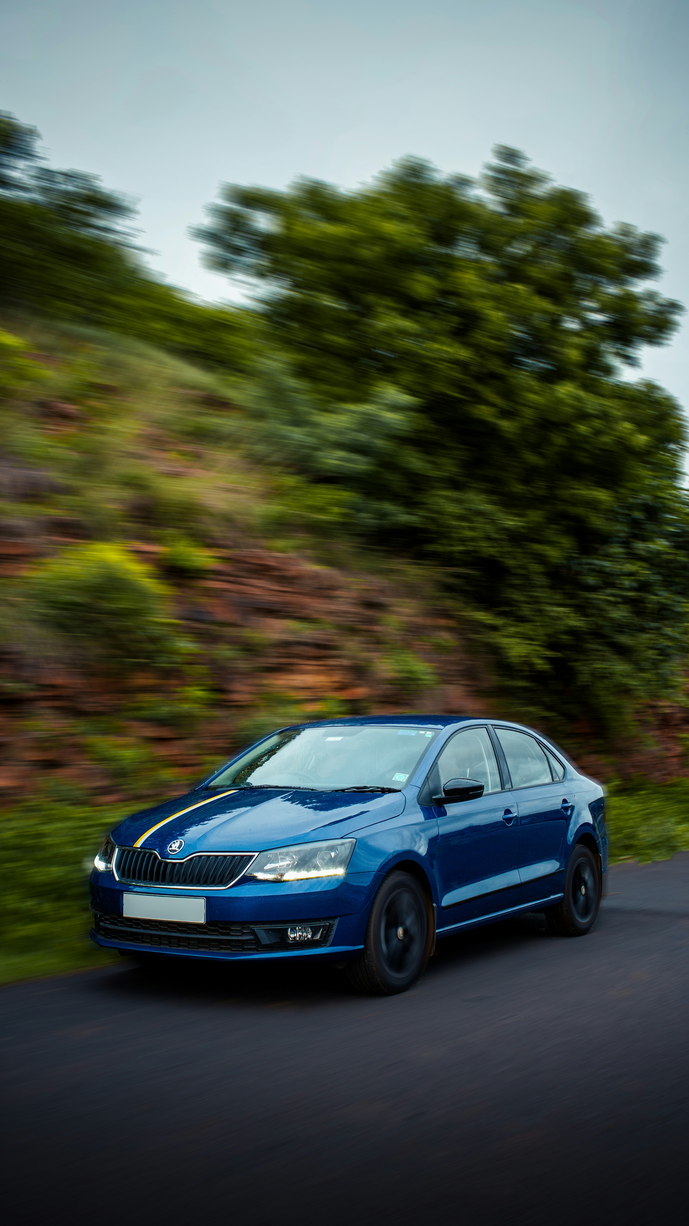 a blue car driving down a road next to trees