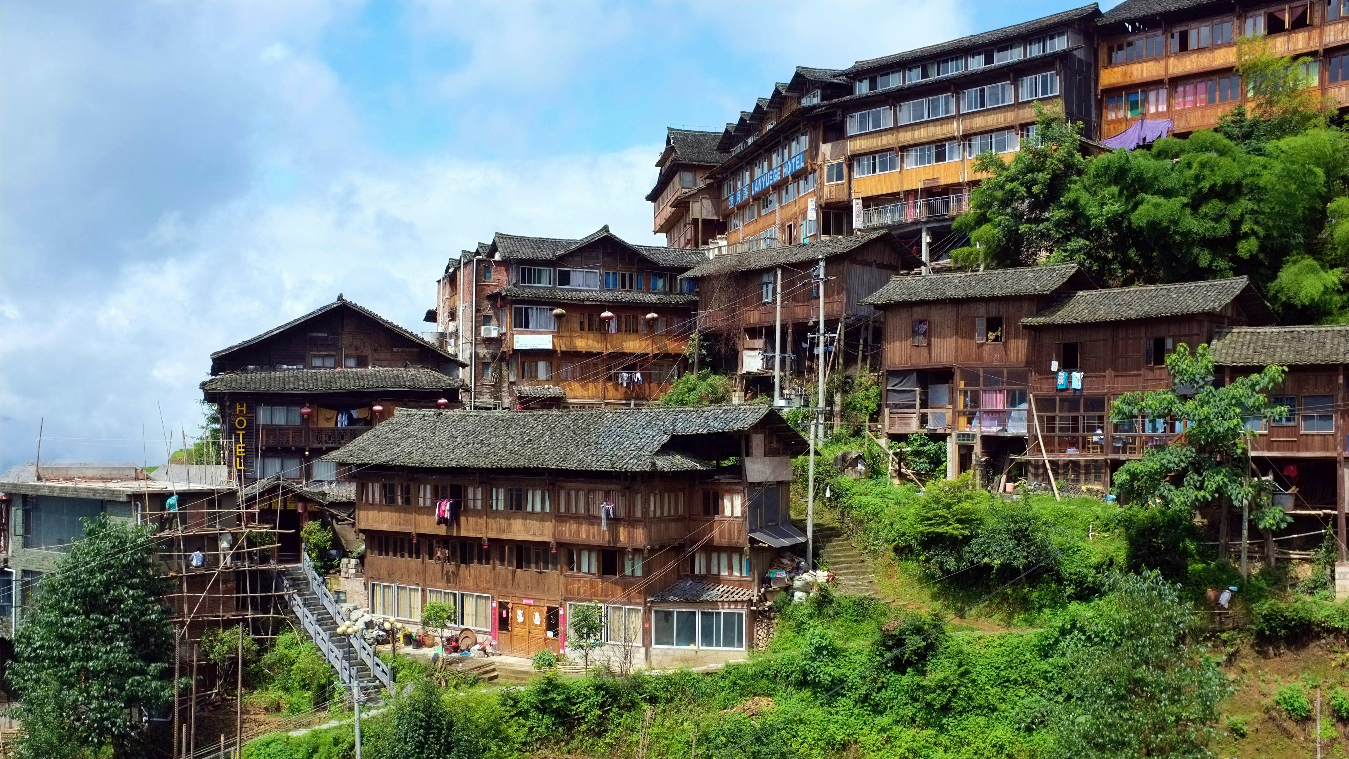 Wooden structures cascading down a lush hillside under a vibrant sky.