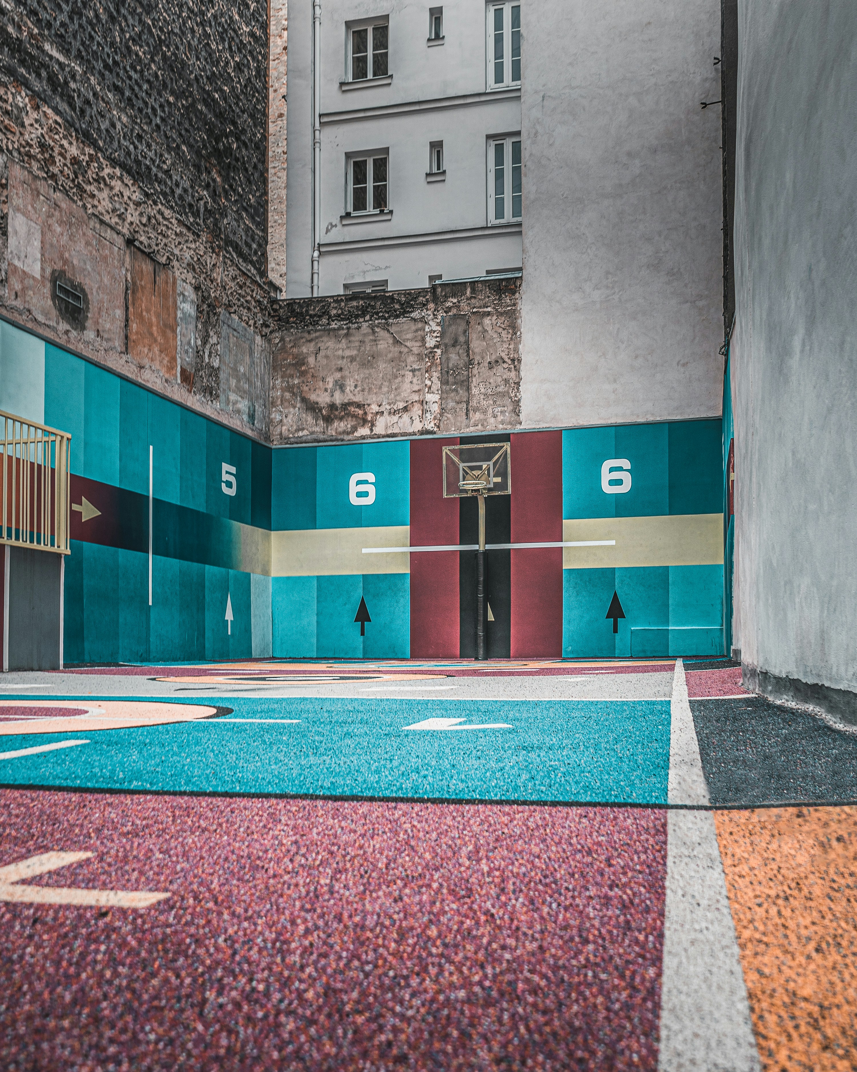 Vibrantly painted basketball court nestled between urban structures, showcasing a unique blend of colors and geometric patterns. The court invites play and creativity.