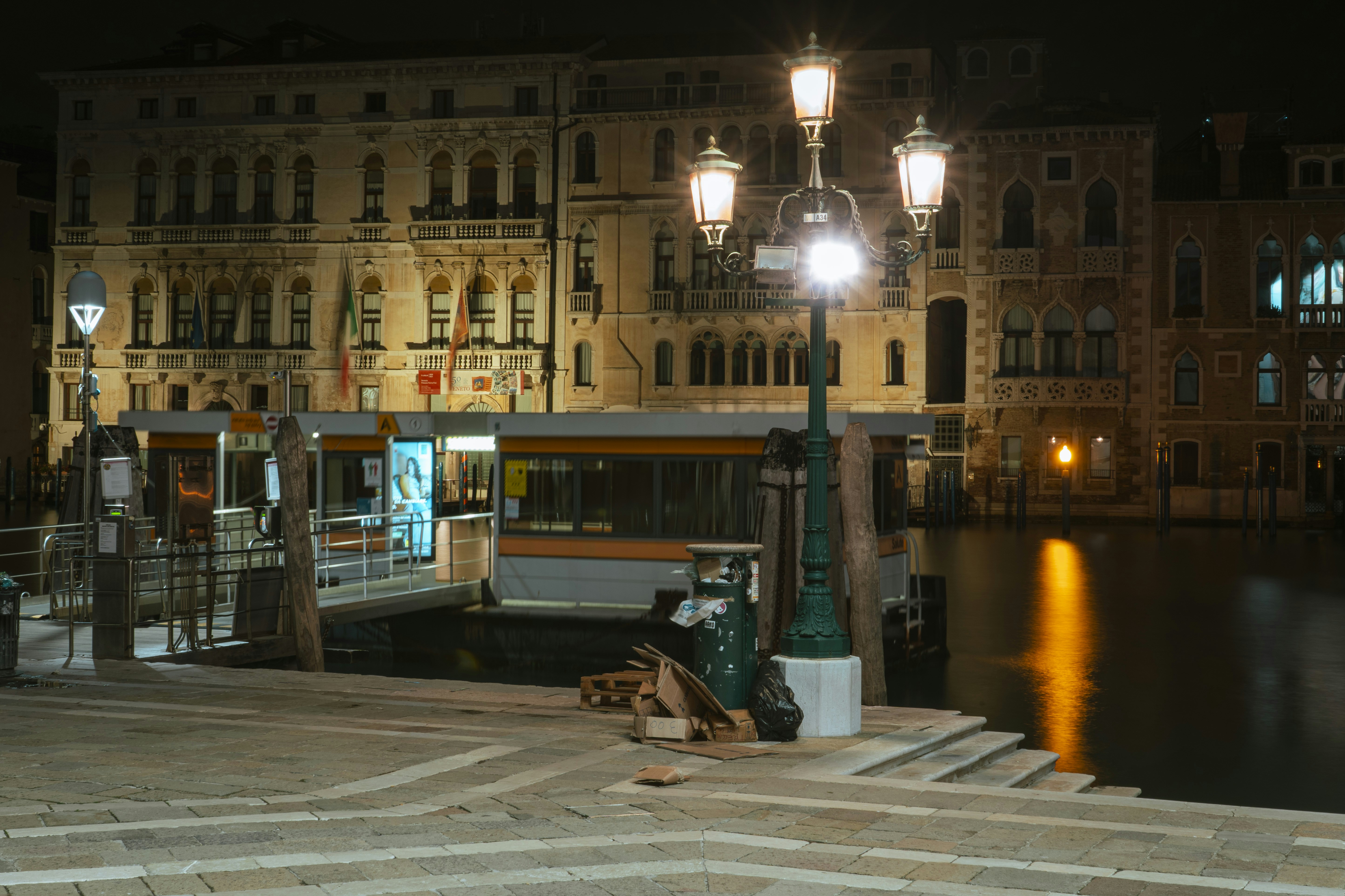Venetian waterfront scene illuminated by vintage street lamps, showcasing architectural elegance and tranquil water reflections.