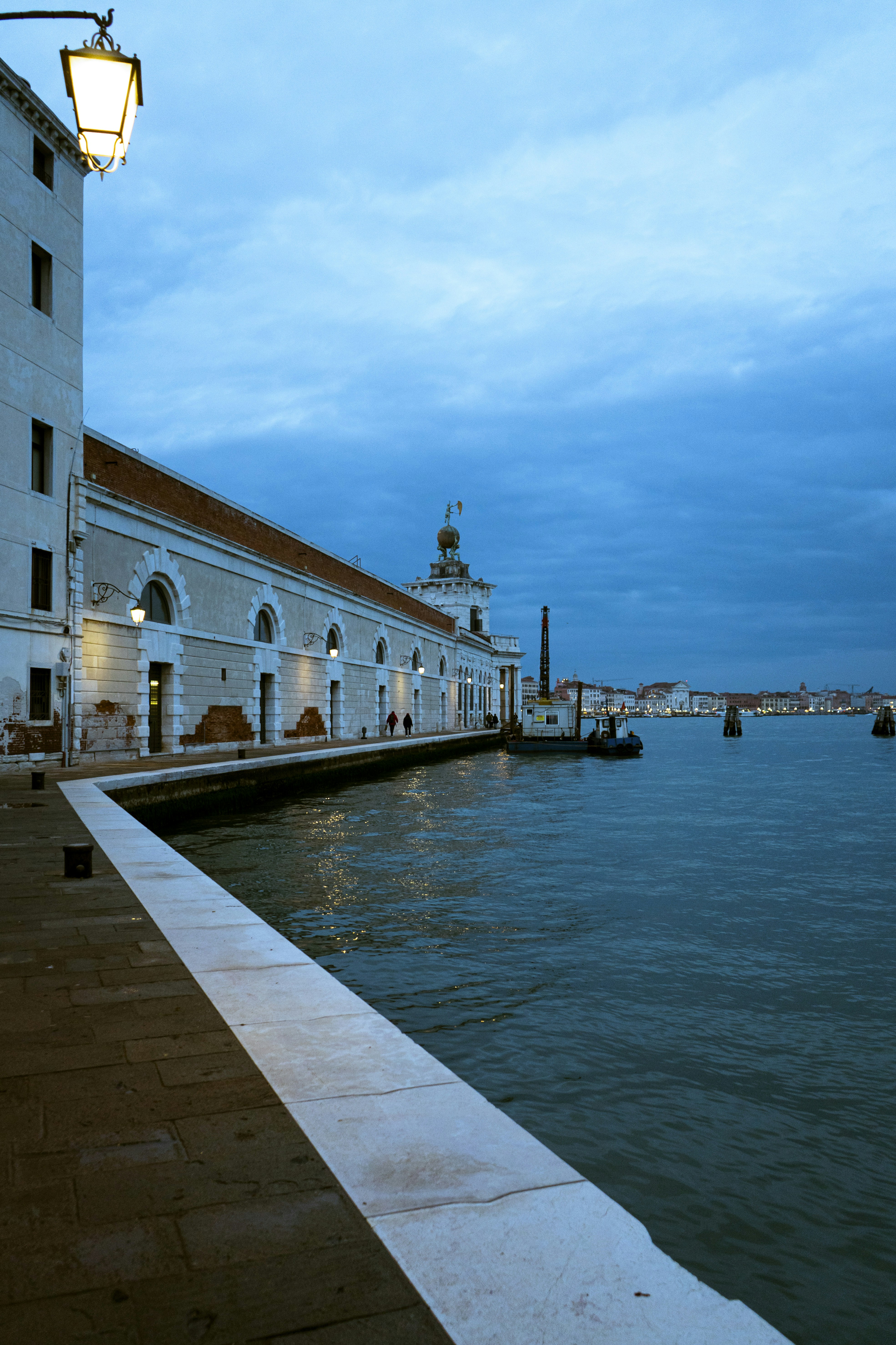 Historic waterfront building illuminated by a streetlamp, with gentle waves reflecting the twilight sky in Venice.