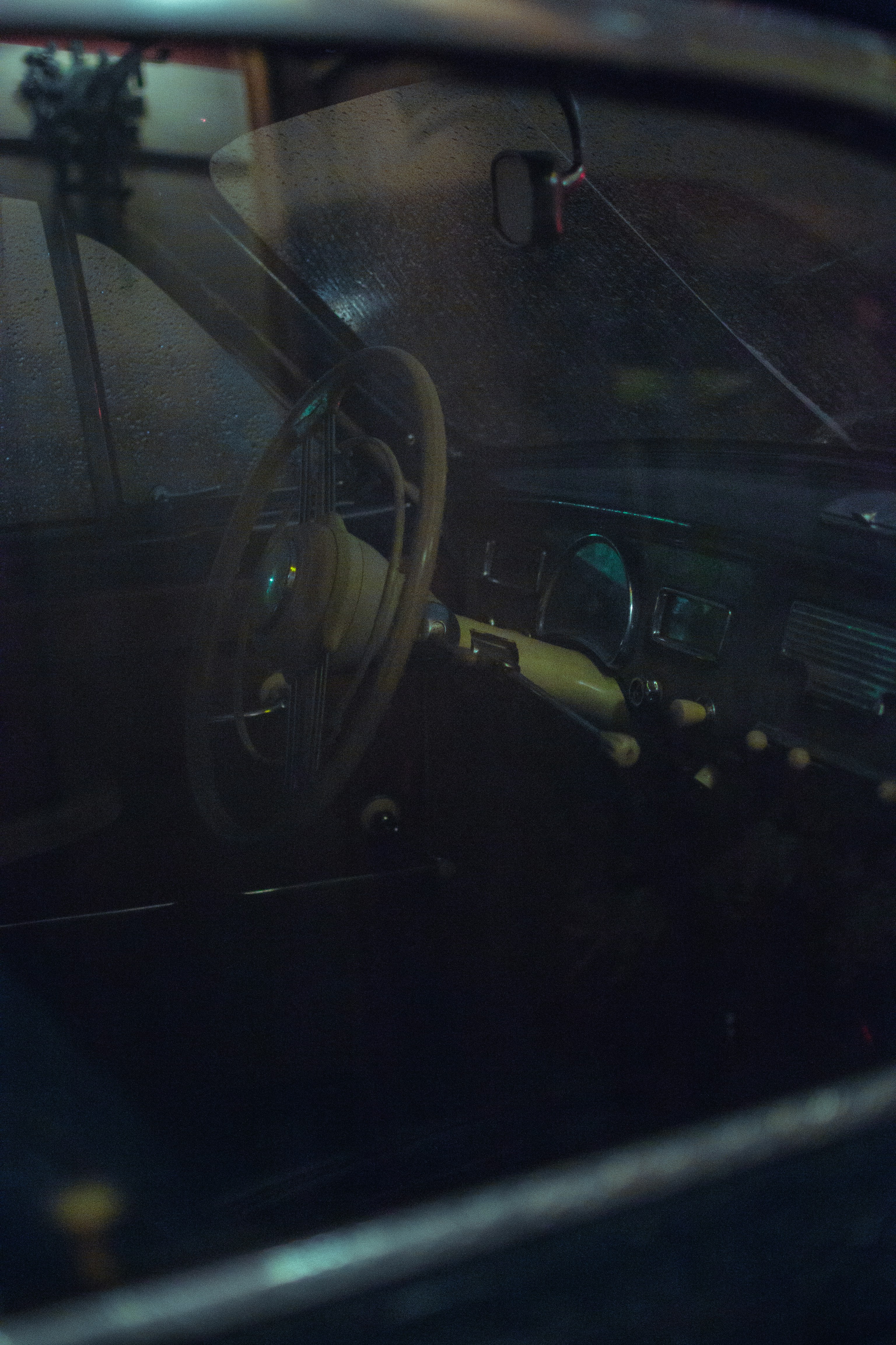 Interior of a vintage car, featuring a classic steering wheel and dashboard, illuminated by soft ambient light and raindrops on the window.