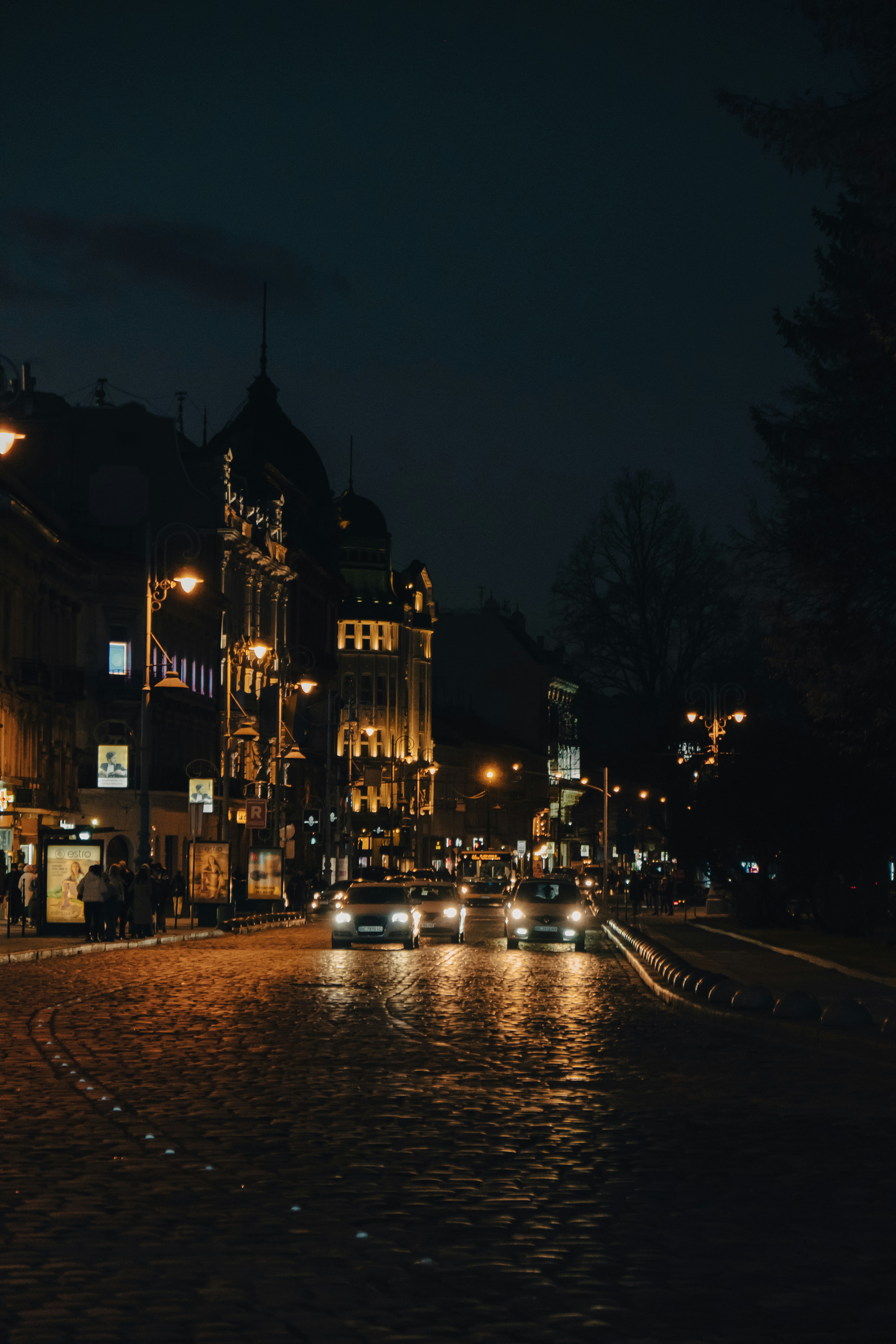 Illuminated street scene featuring vintage architecture and moving vehicles under a night sky.