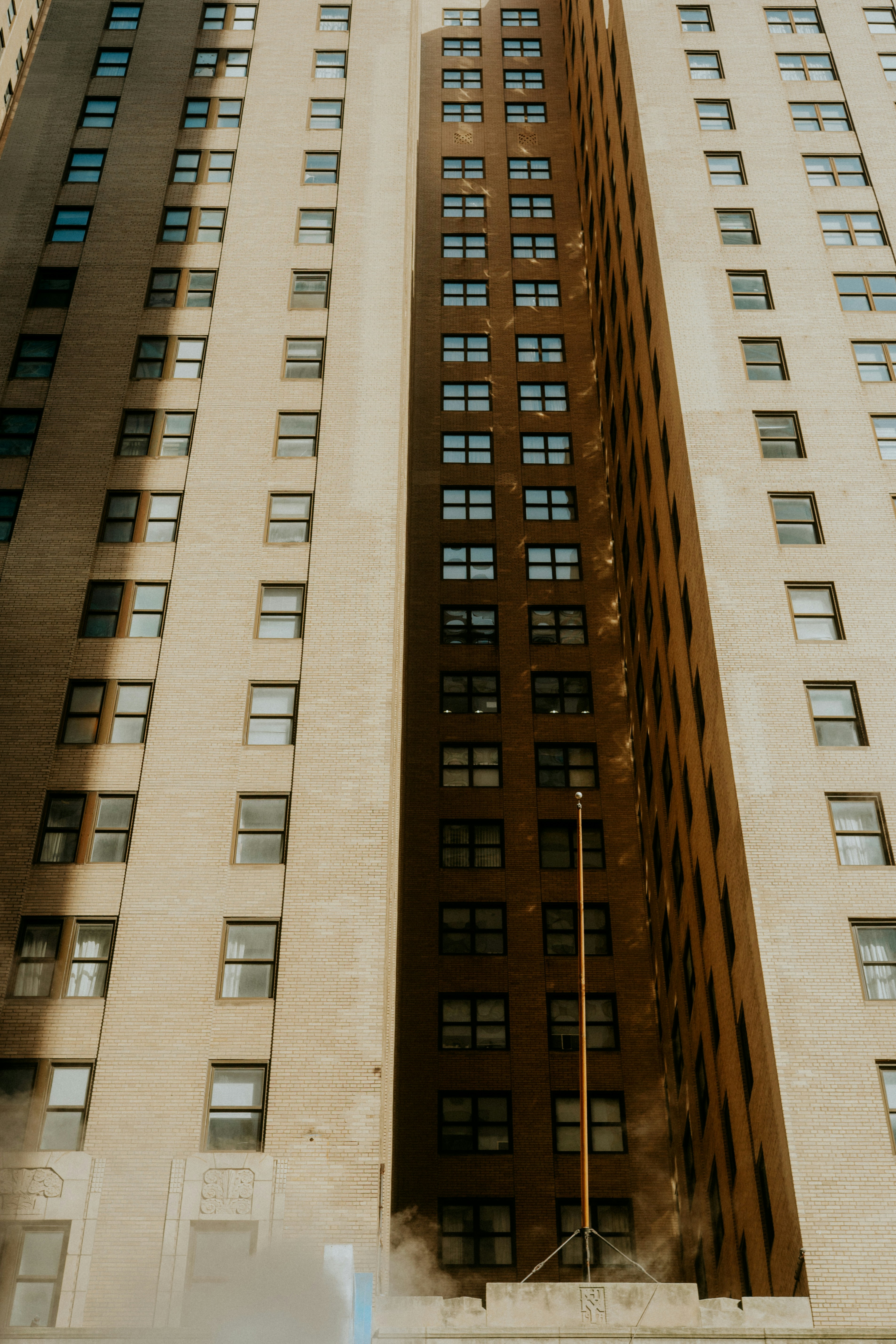 Tall building facade showcasing a blend of brick and modern window designs, with a flagpole adding a touch of character.