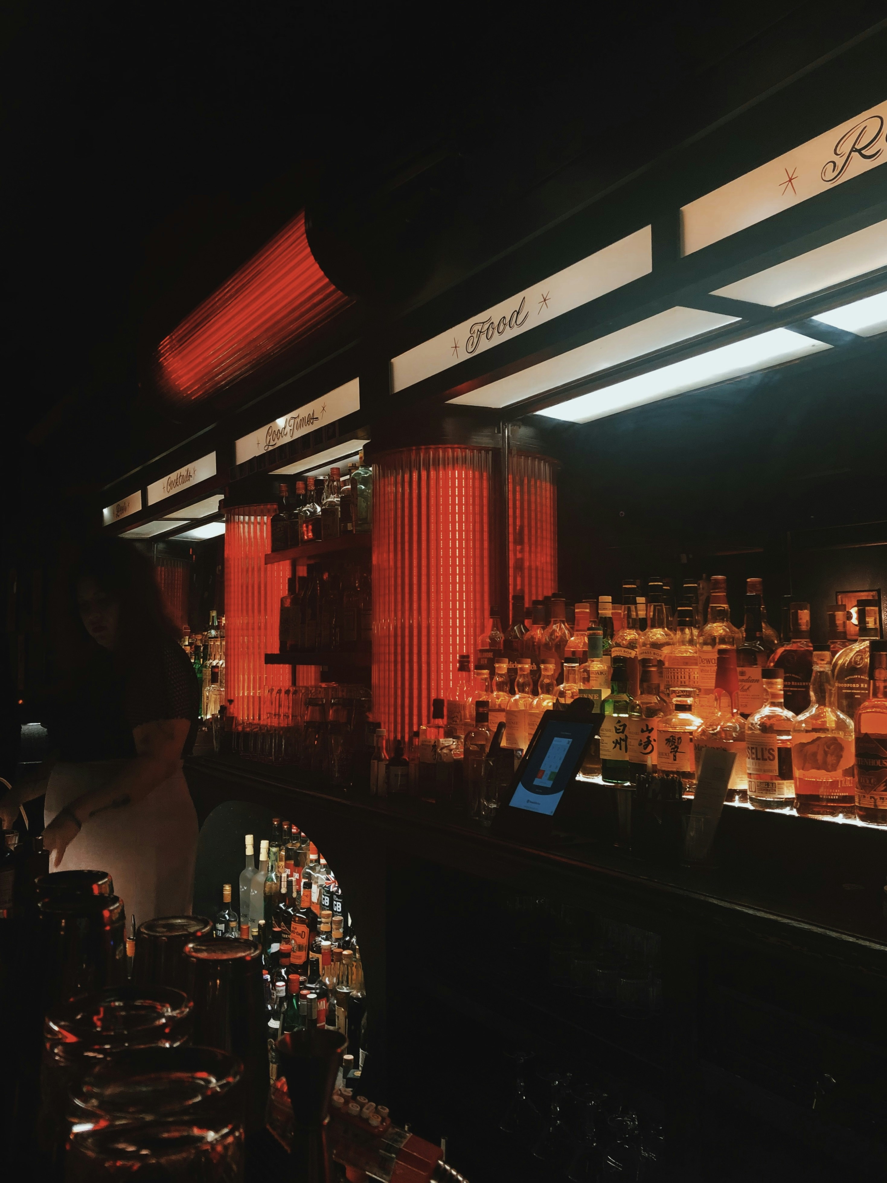 A vibrant bar scene showcasing a variety of illuminated liquor bottles against a dark backdrop. The ambiance is enhanced by warm red lighting.