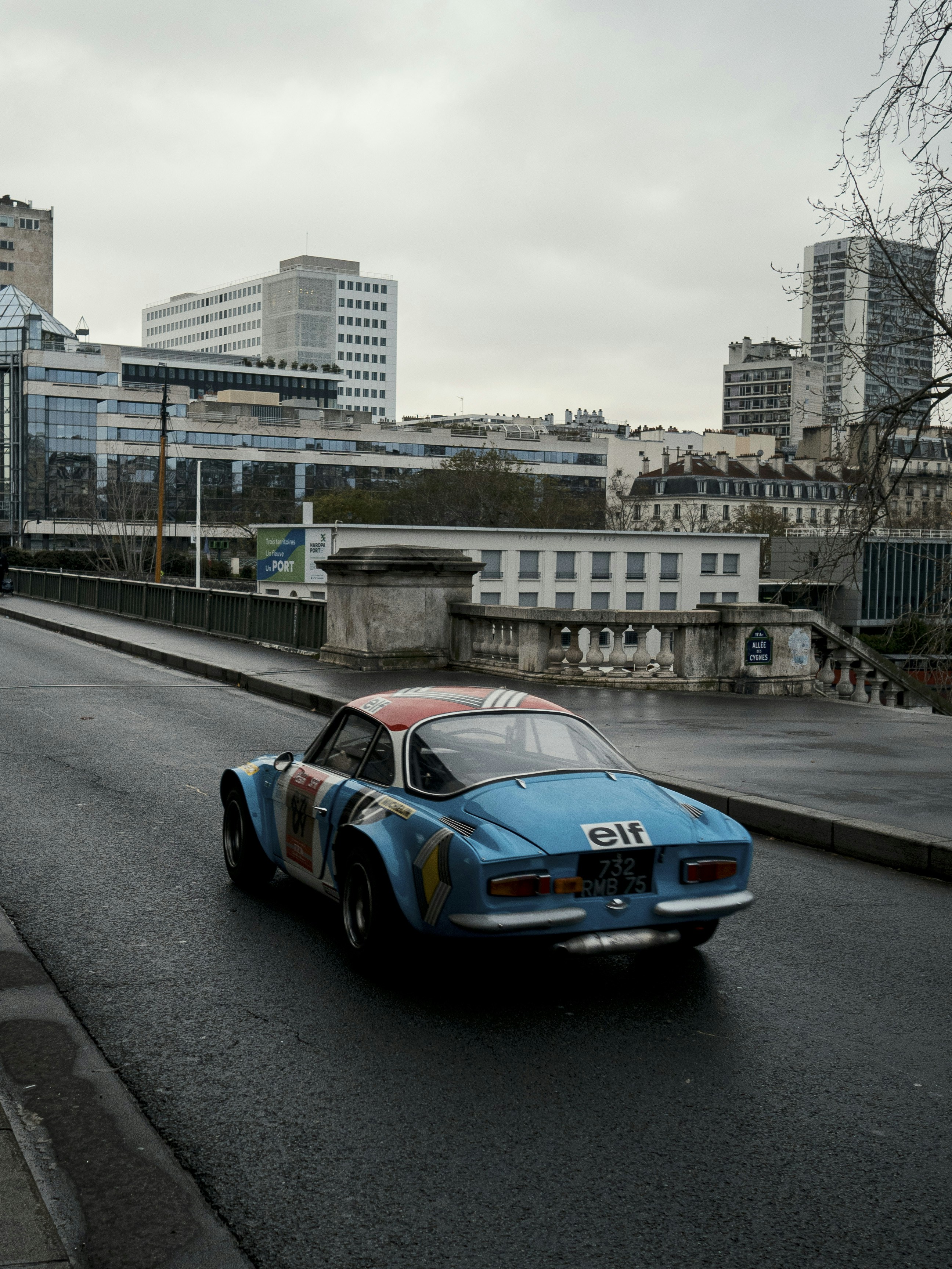 Classic blue racing car navigating a quiet city street under overcast skies.