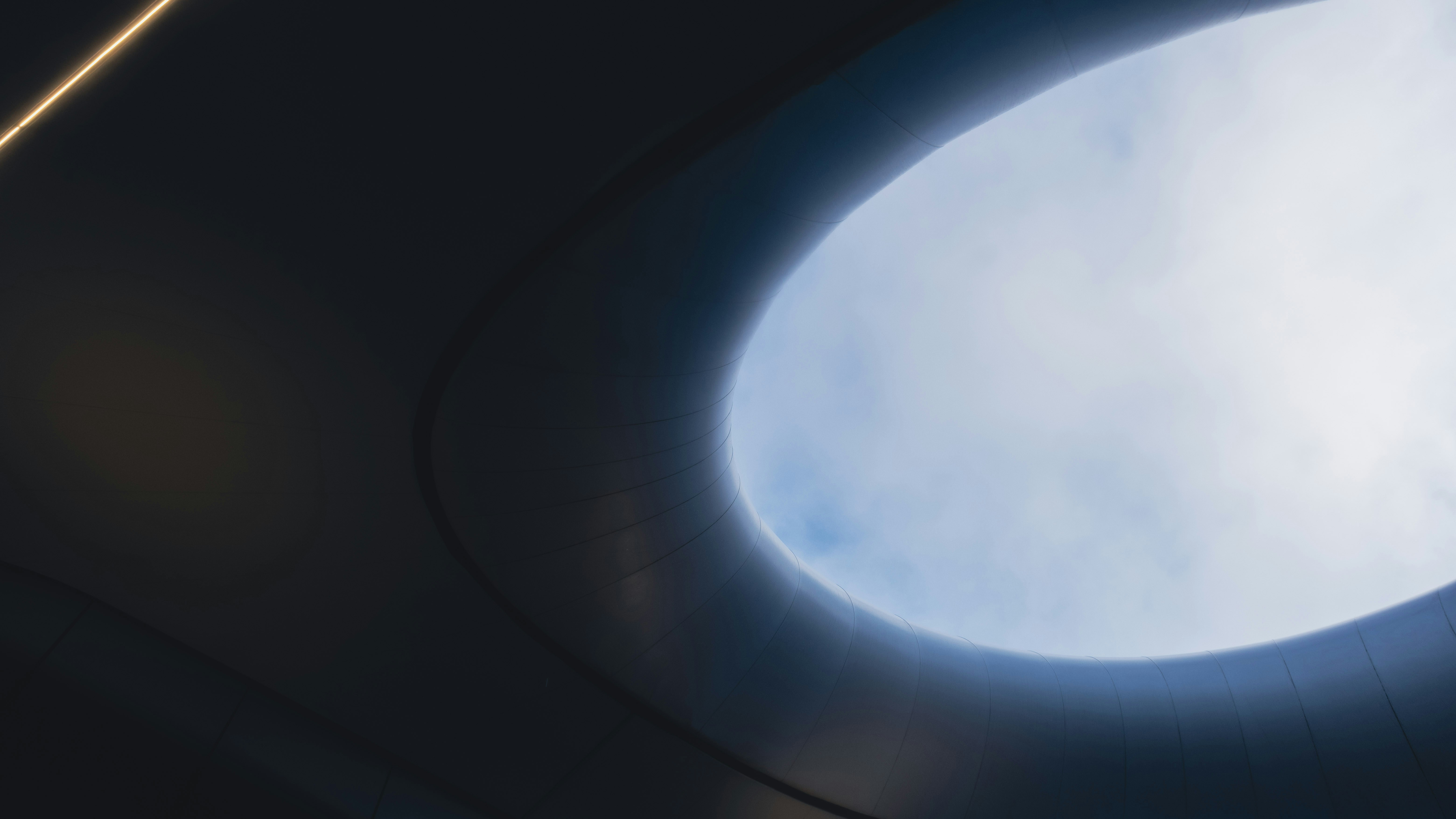 Circular opening in a modern architectural structure revealing a cloudy sky above.