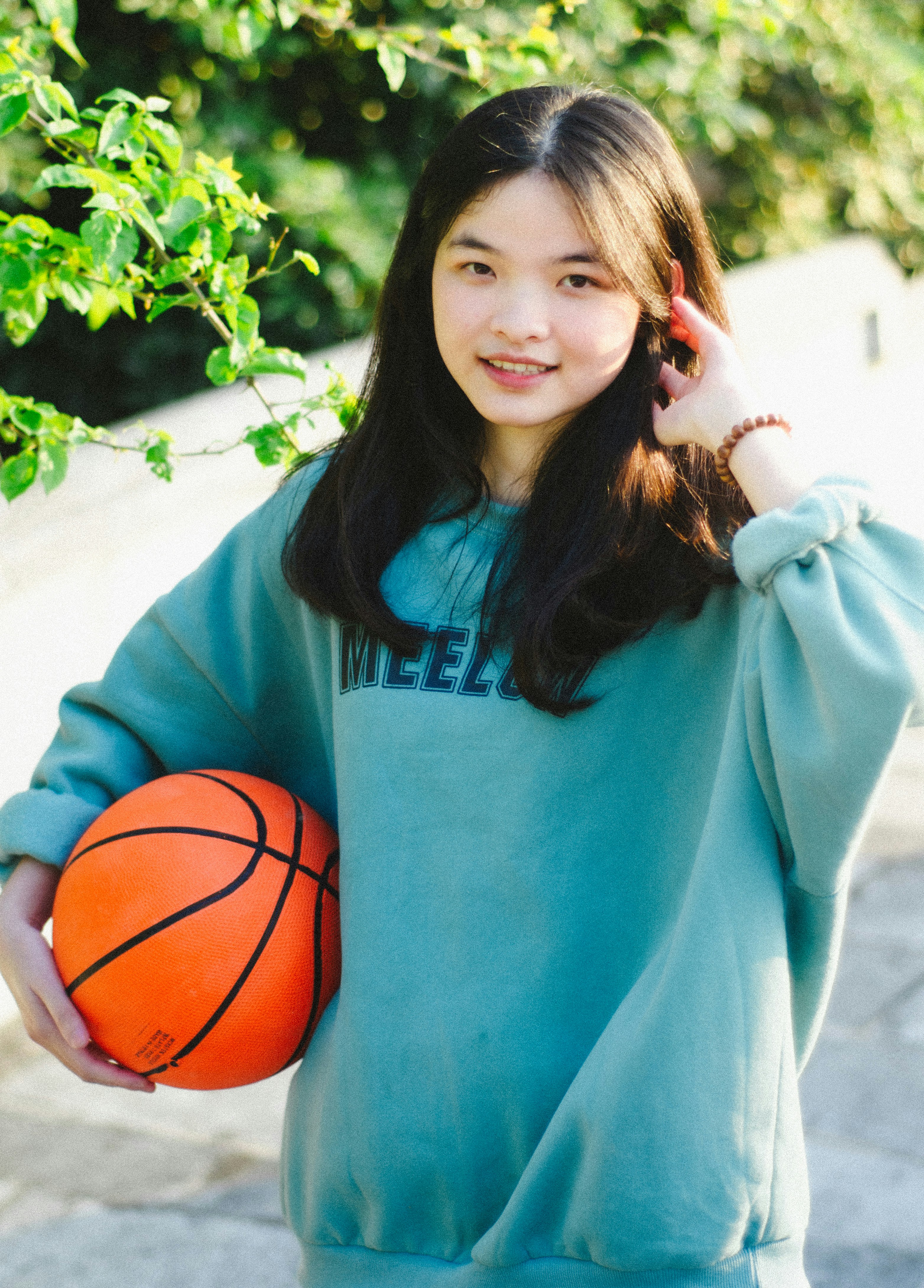 a young woman holding a basketball while standing next to a tree