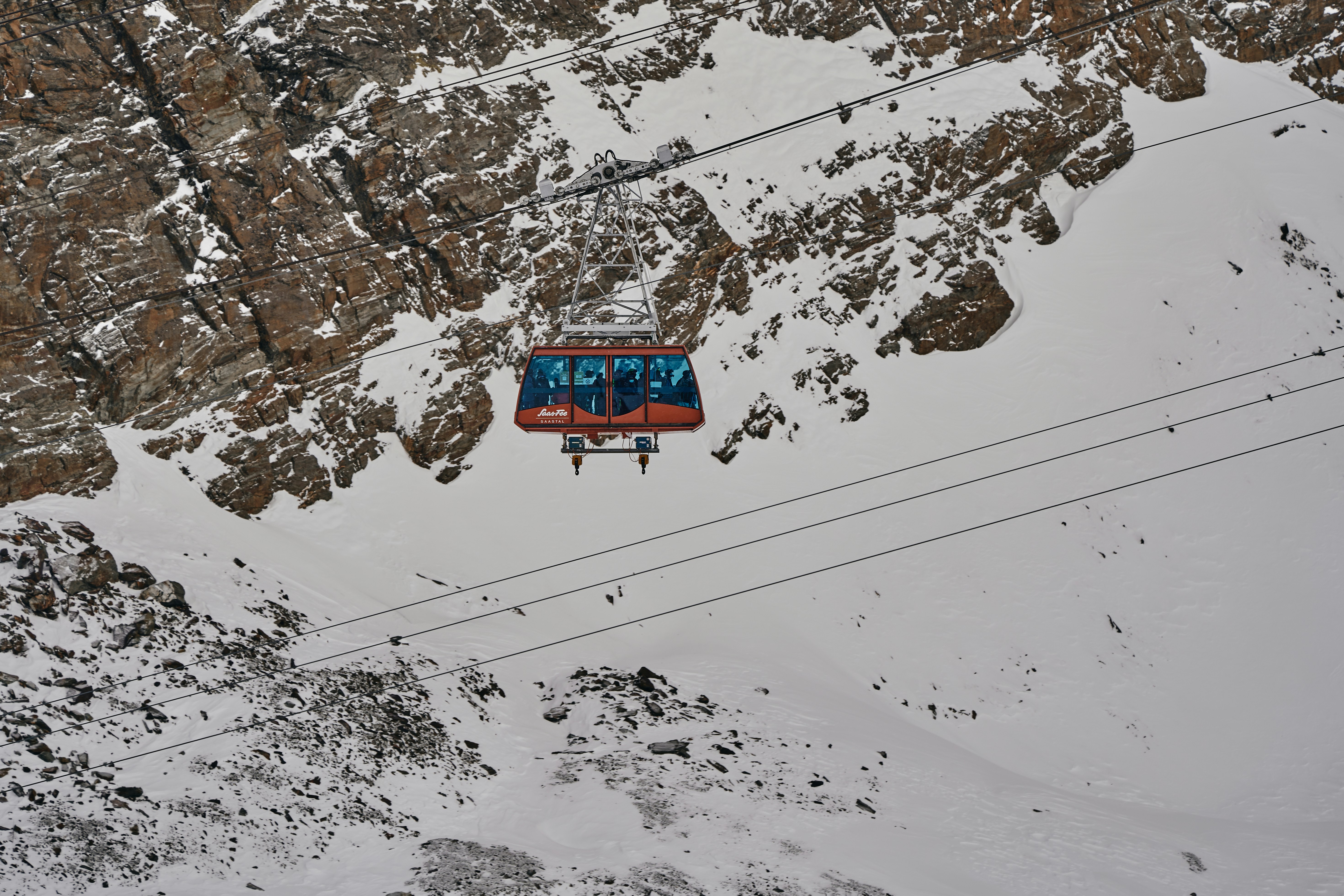 A gondola gliding over a snowy landscape, suspended against rugged mountain terrain. The scene captures the thrill of alpine adventures.