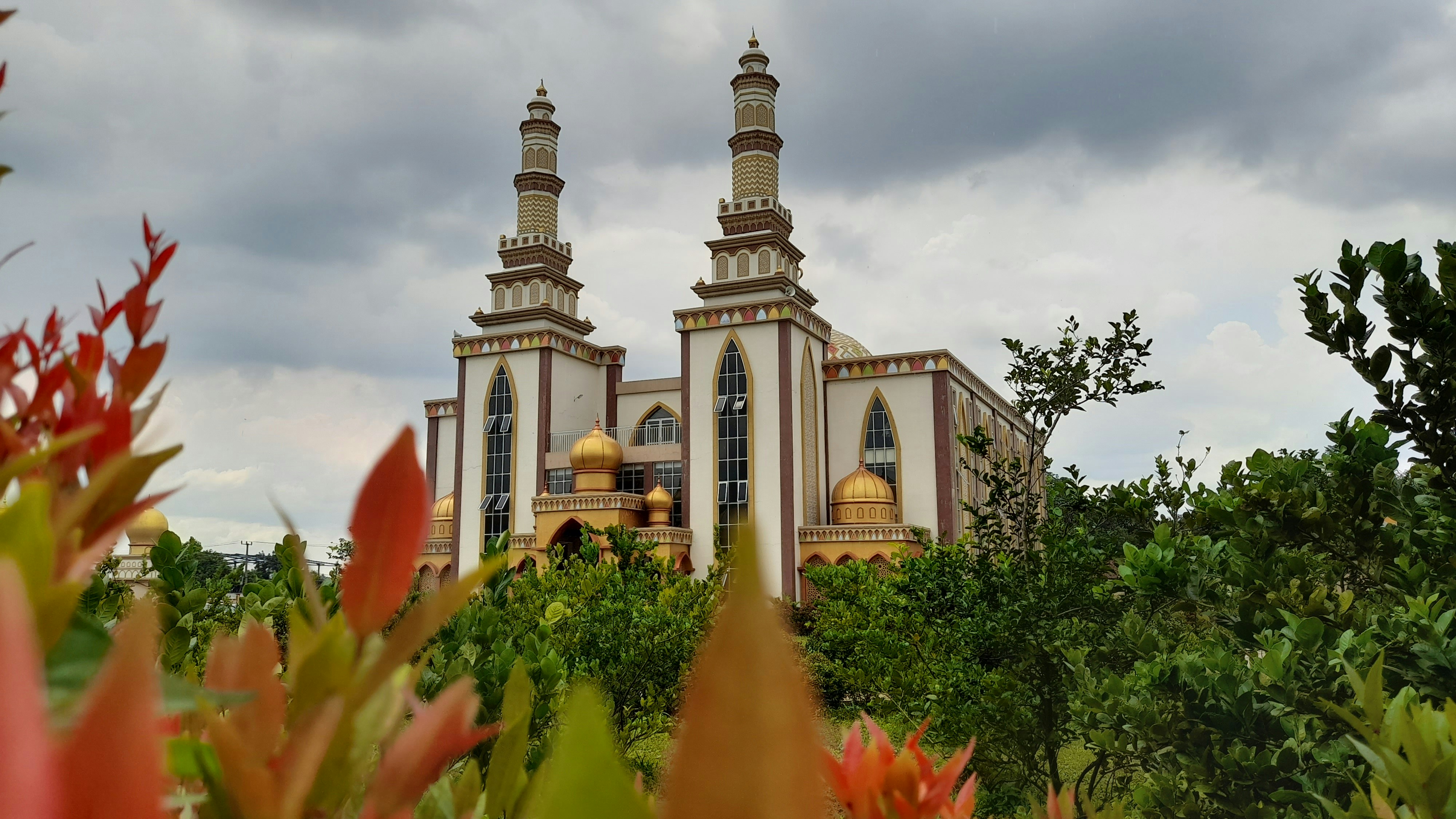 Intricate architectural towers rise above lush greenery under a cloudy sky.