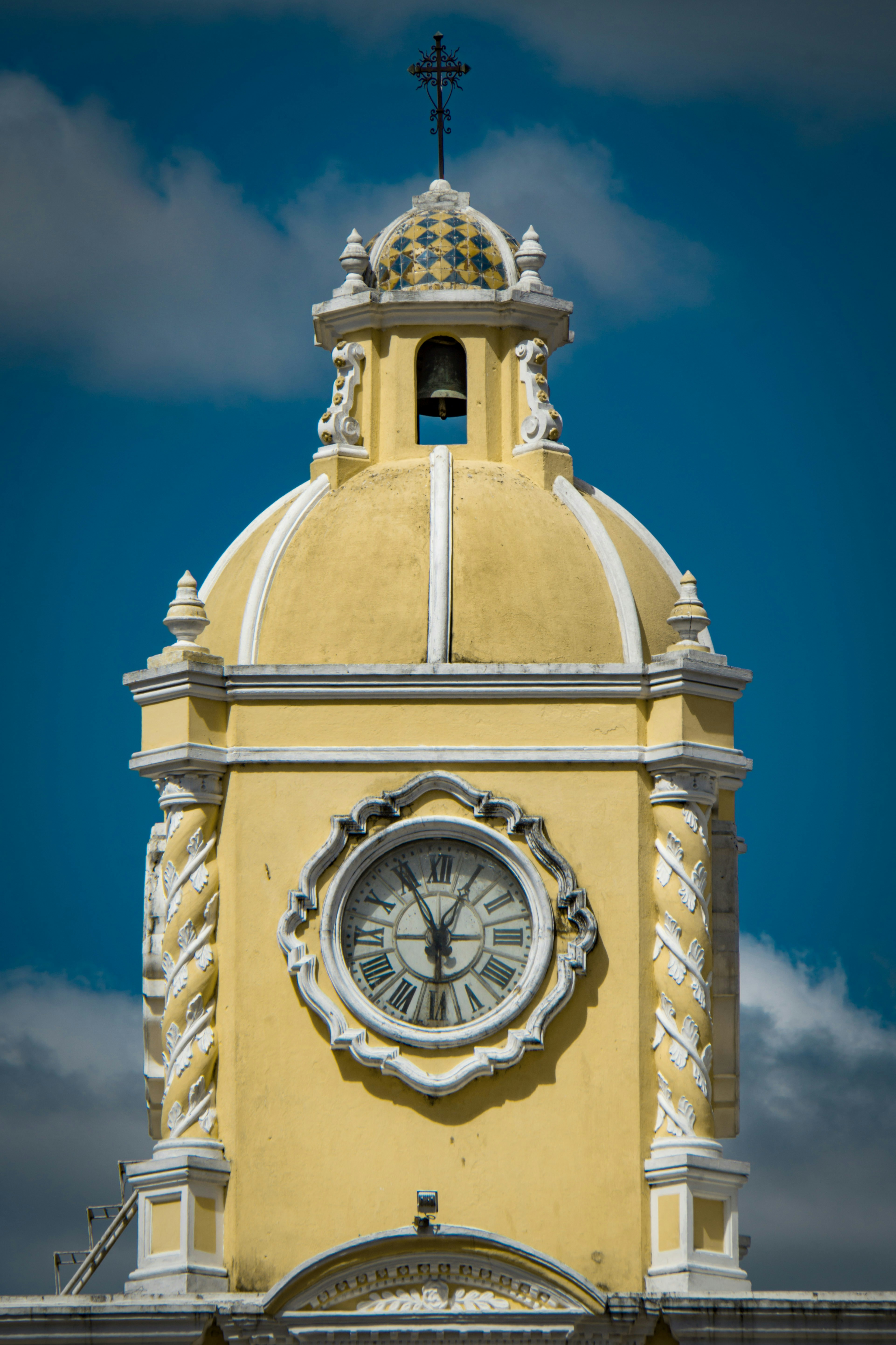 Ornate yellow clock tower with a prominent clock face and decorative dome, set against a blue sky.