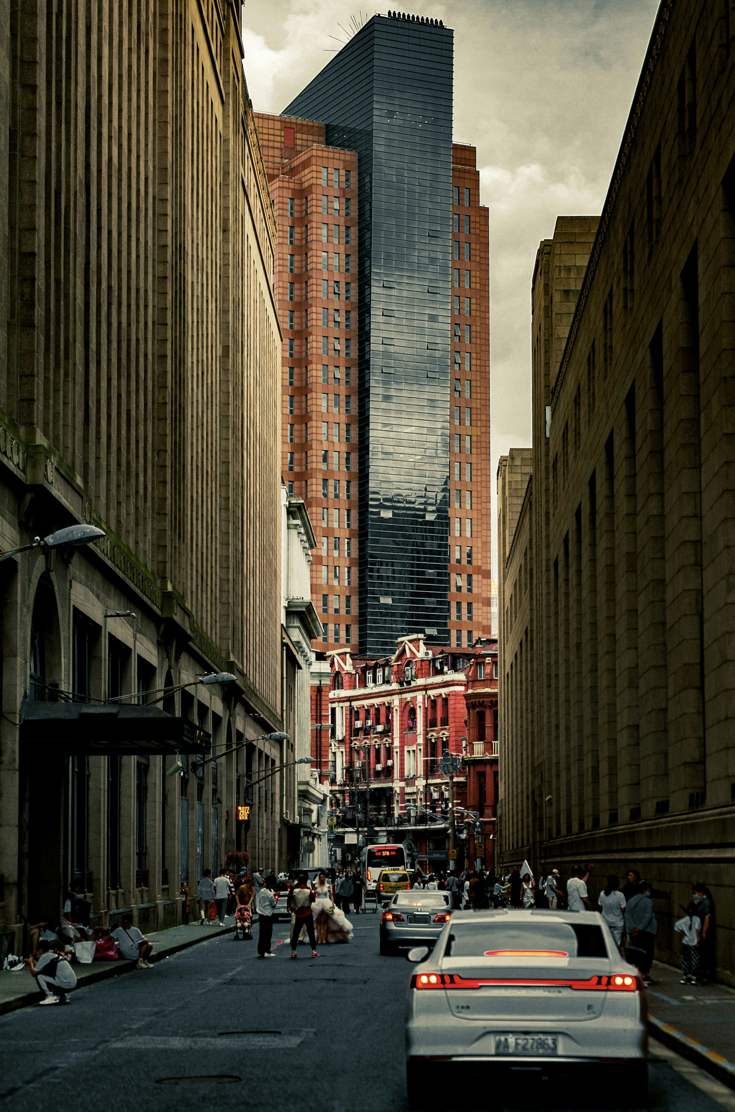 A bustling city street framed by towering skyscrapers, showcasing a blend of modern architecture and historic buildings. The scene captures the vibrant life of urban dwellers.