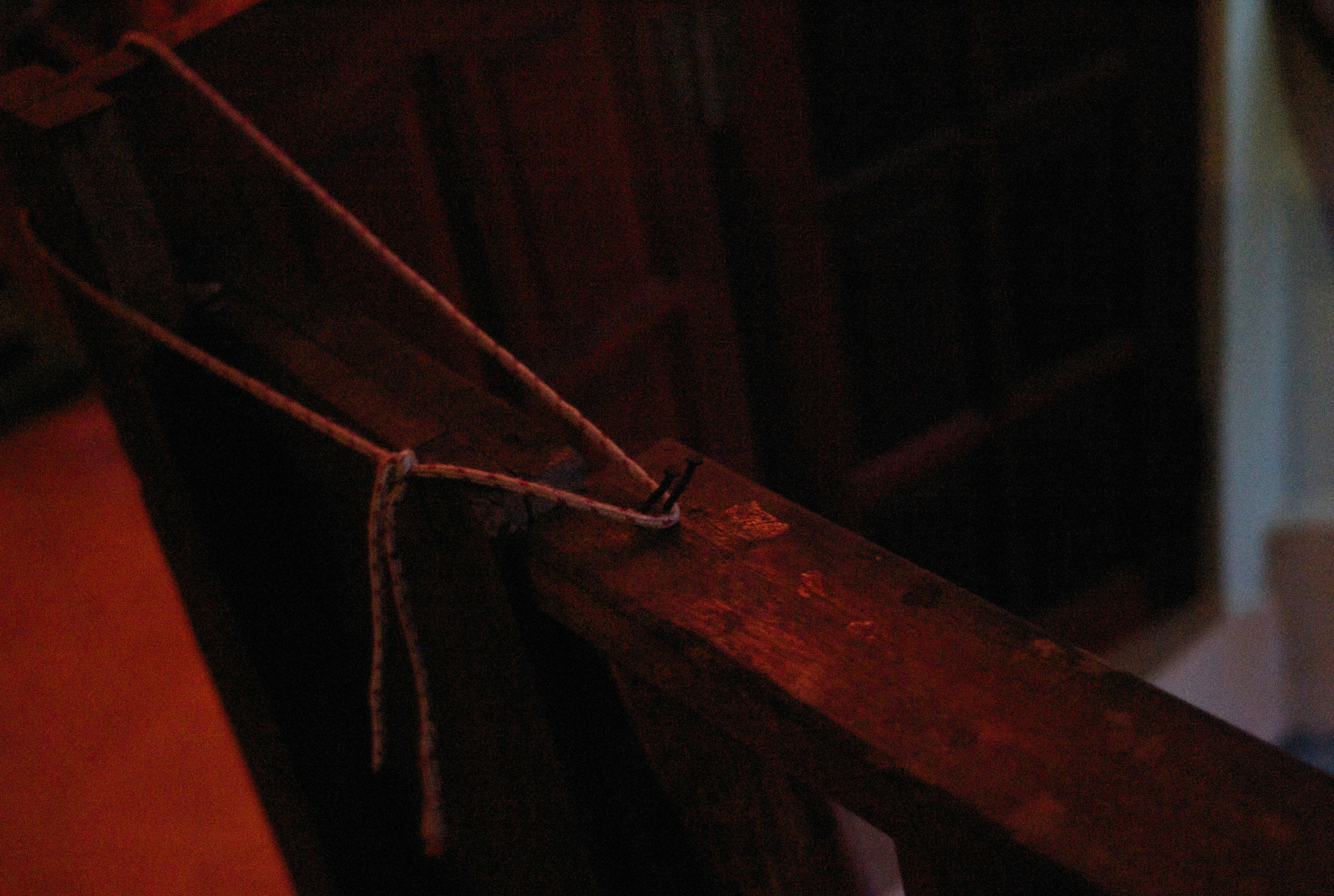Close-up of a weathered wooden railing with a frayed rope tied around a post, bathed in warm red light in a dim interior.