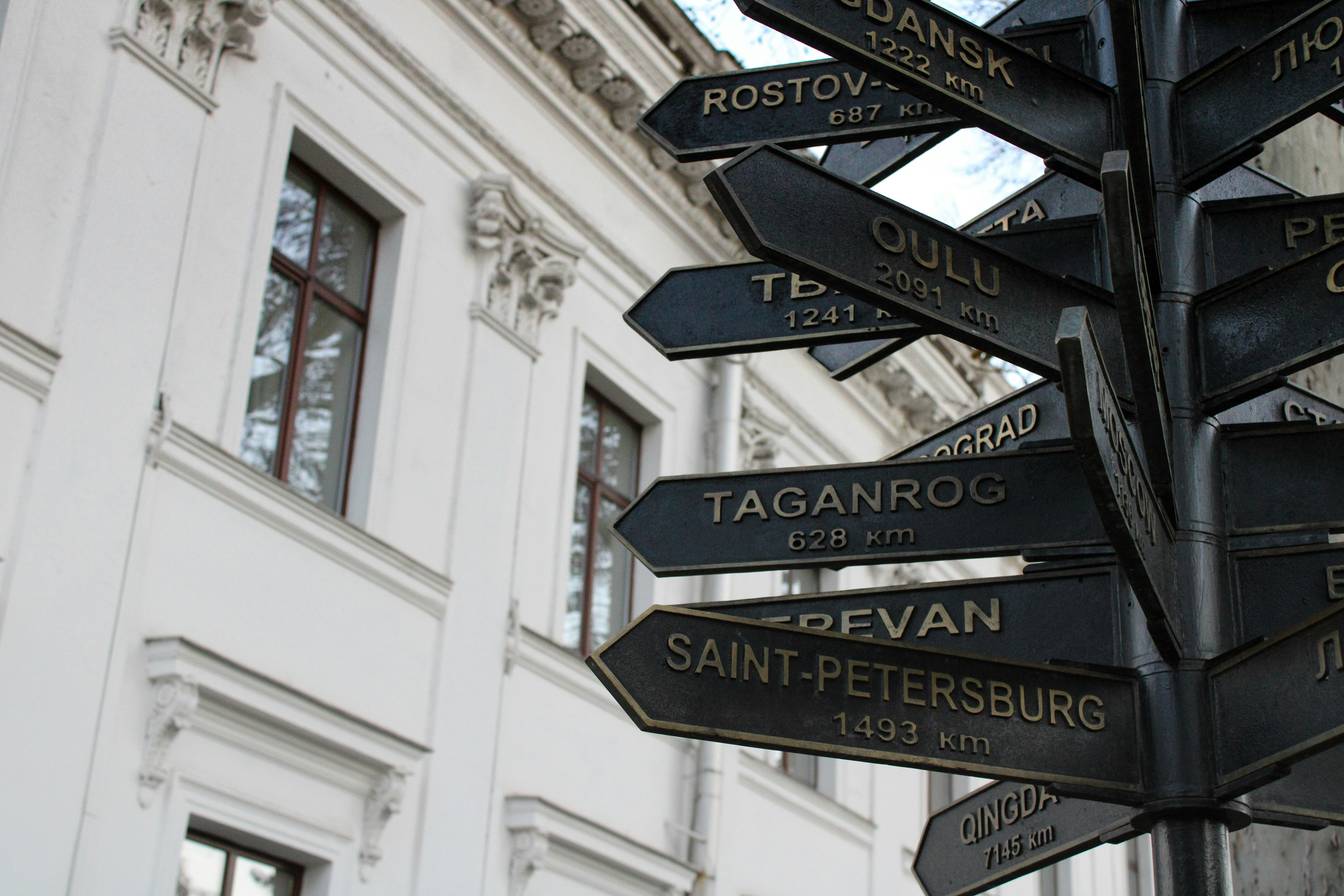 Directional signpost displaying distances to various cities, set against a historic building backdrop.